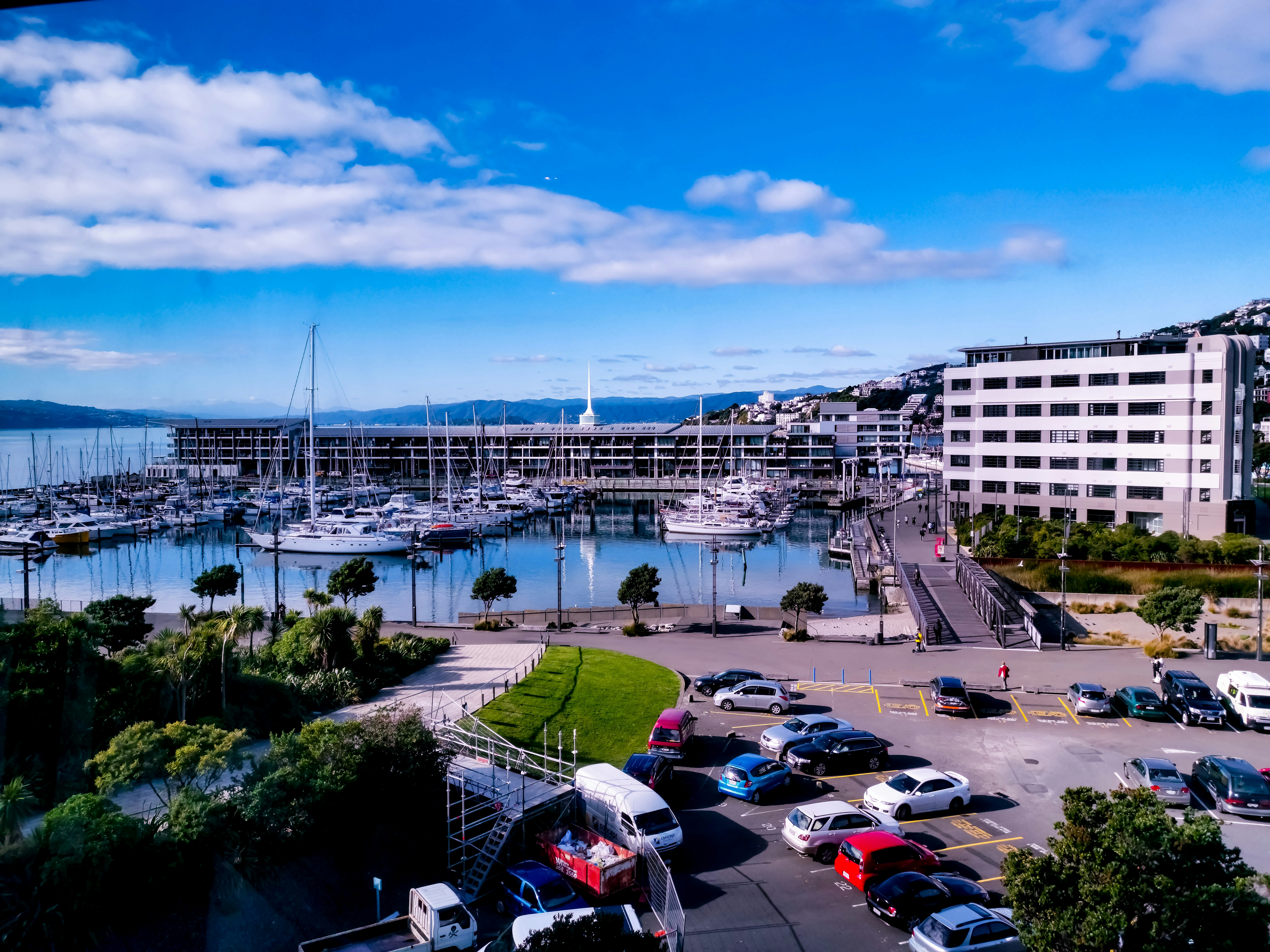 Marina with docked sailboats alongside urban buildings under a vibrant blue sky.