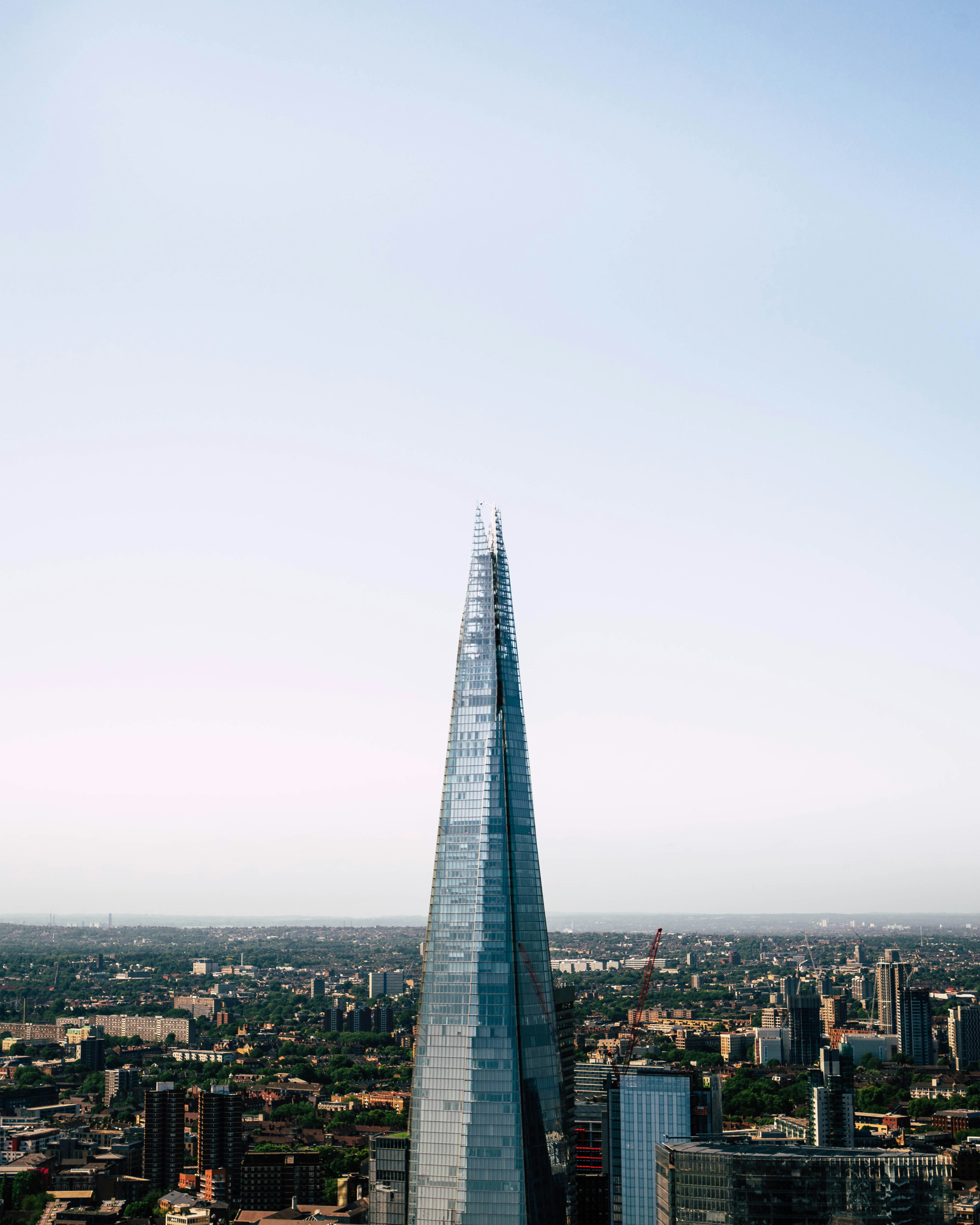 The Shard pierces the skyline, showcasing its sleek glass façade against a pale blue sky. Surrounding buildings provide a contrasting urban landscape.