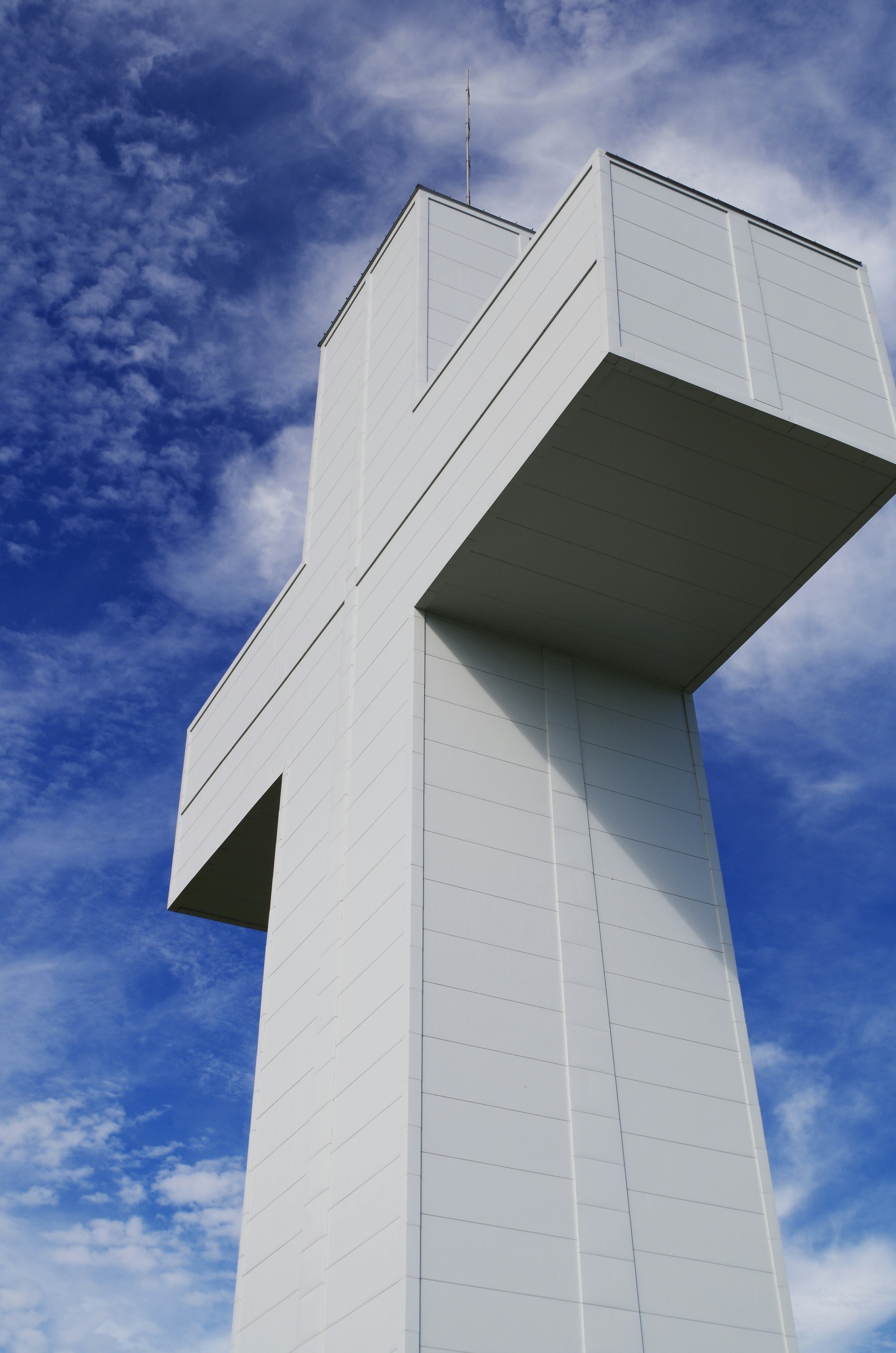 Sleek white cross structure rises against a backdrop of blue sky and scattered clouds.
