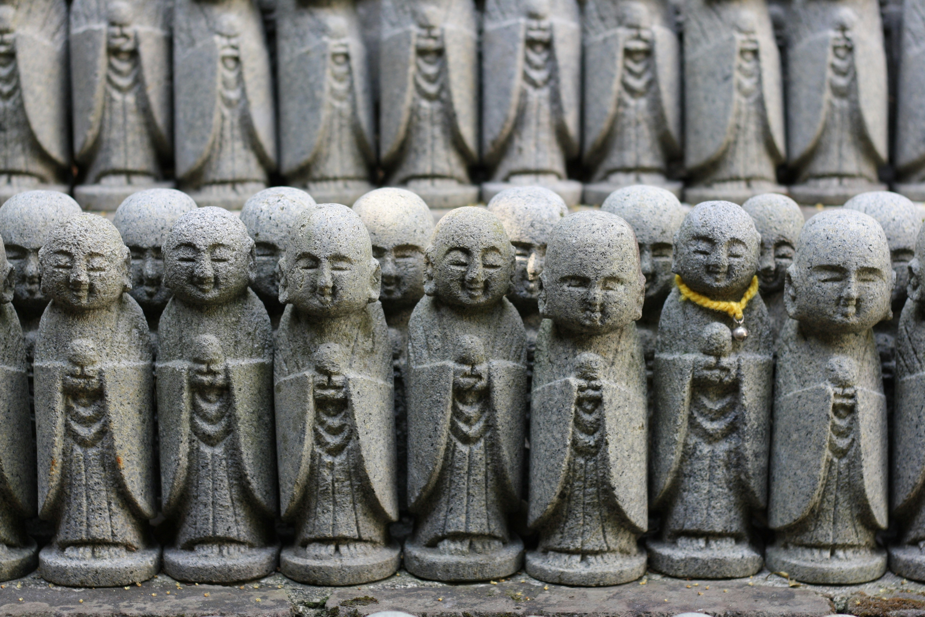 A multitude of stone figurines representing serene figures, arranged in a harmonious pattern, with one adorned in a golden necklace.