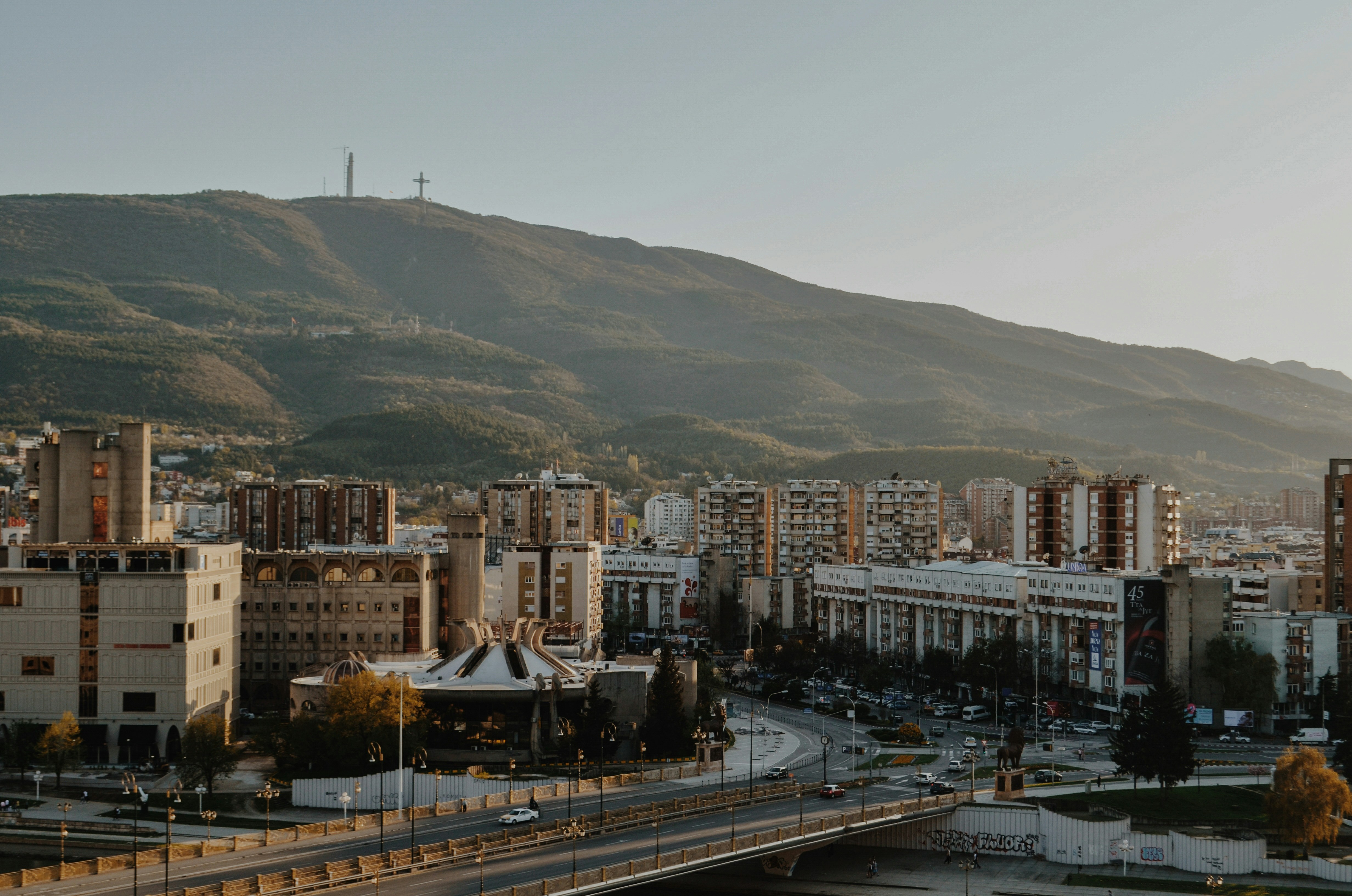 Cityscape with a backdrop of rolling hills under a clear sky, captured in soft morning light.