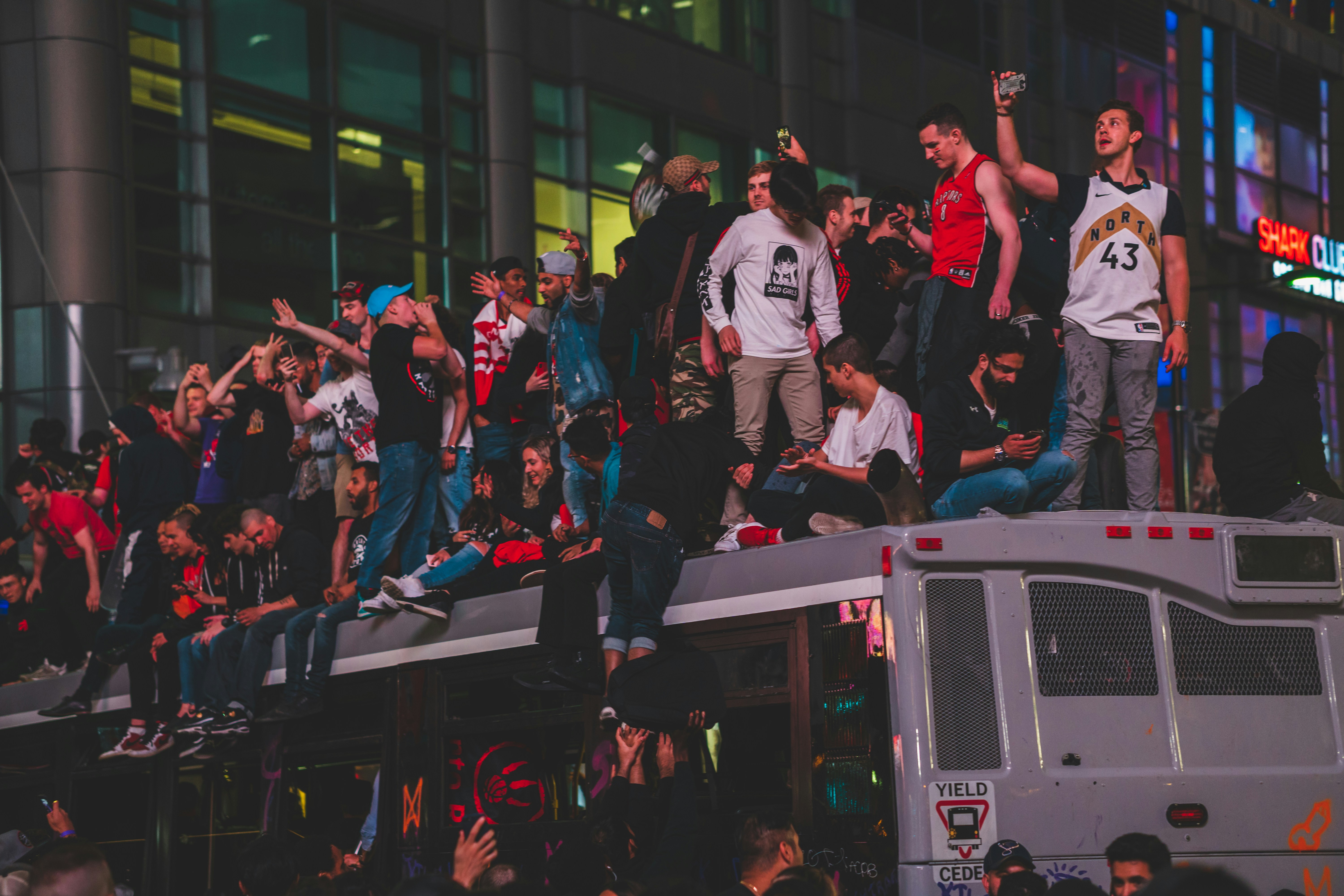 Crowd celebrating atop a bus in a city at night, with vibrant lights illuminating the scene.
