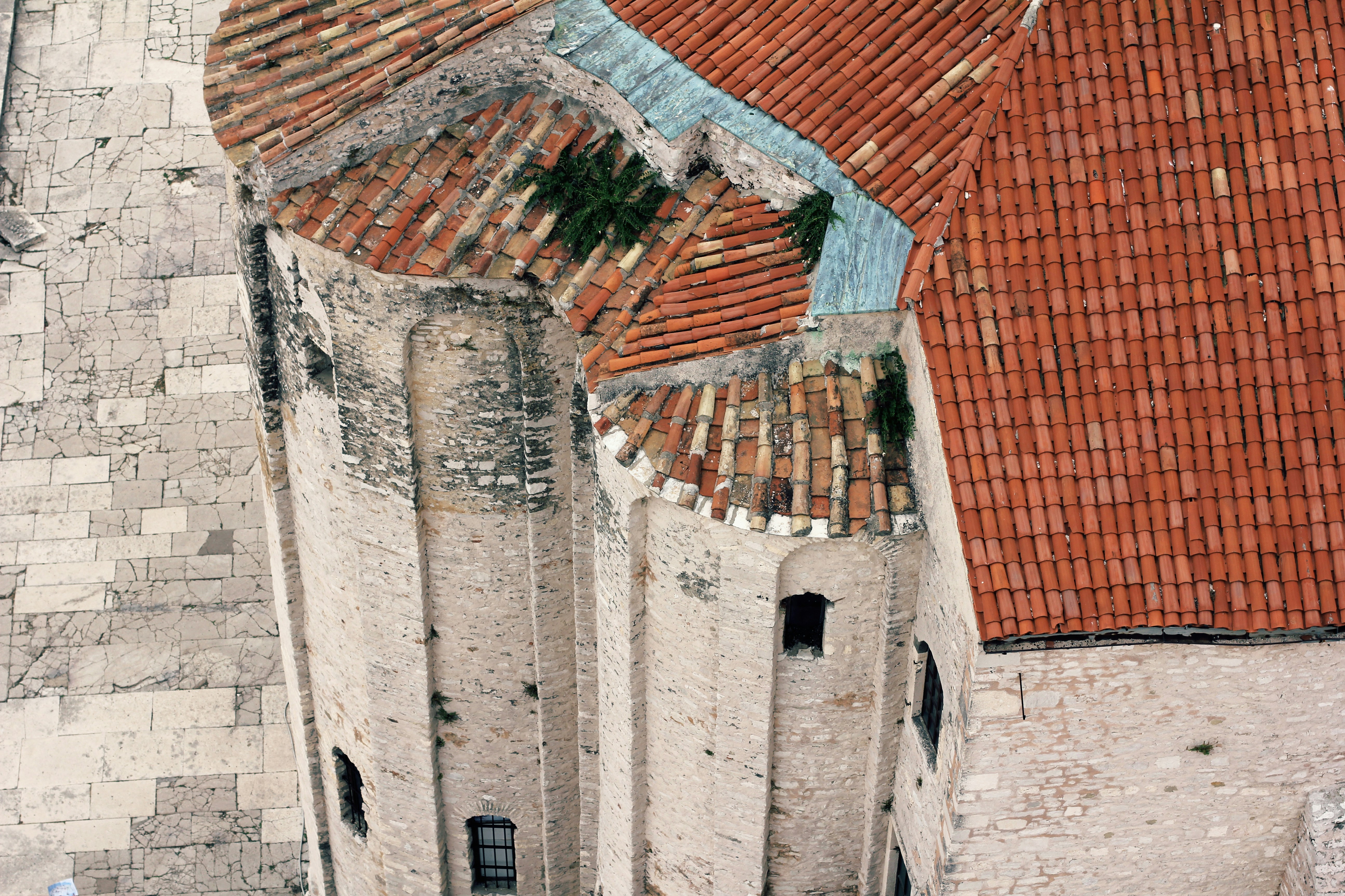 Aerial view of an ancient stone tower with a red-tiled roof and weathered textures.