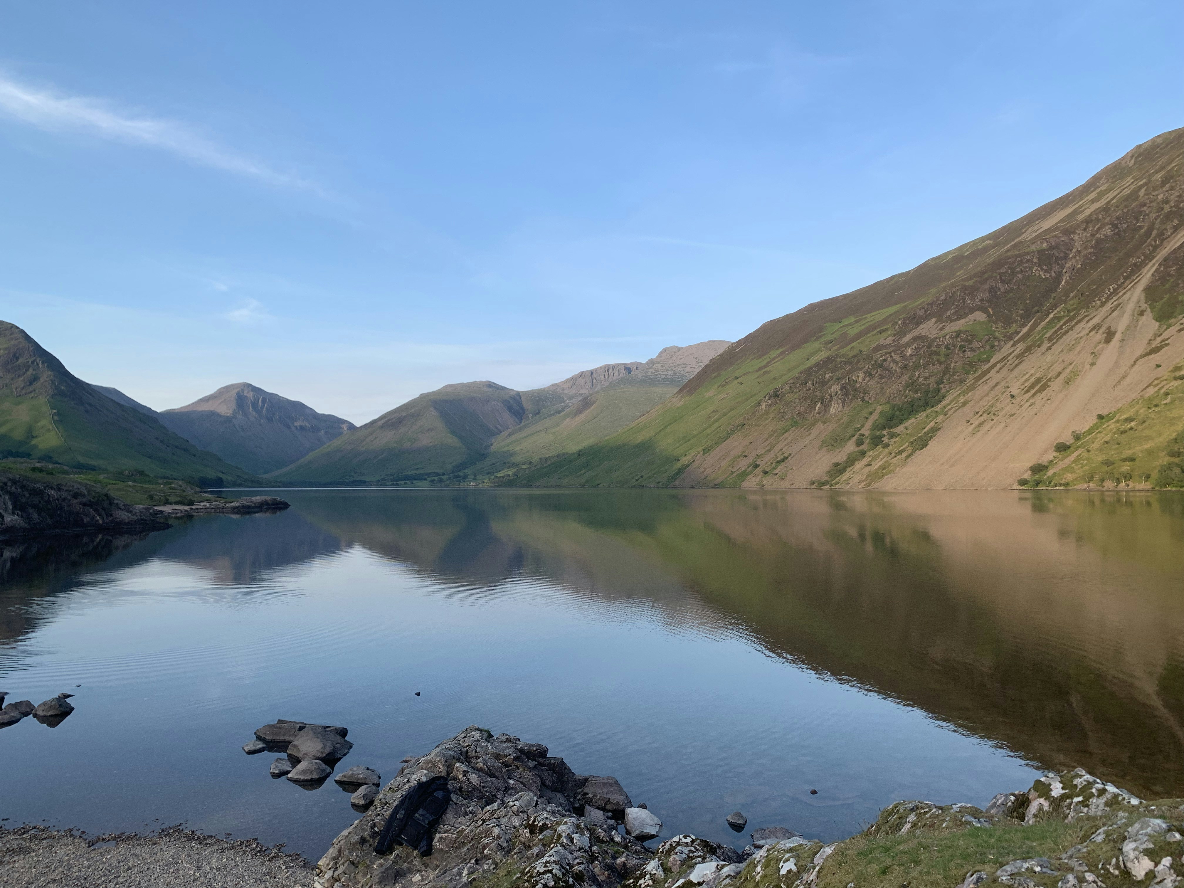 Tranquil lake reflecting the surrounding hills under a clear blue sky, showcasing the beauty of nature's landscape.