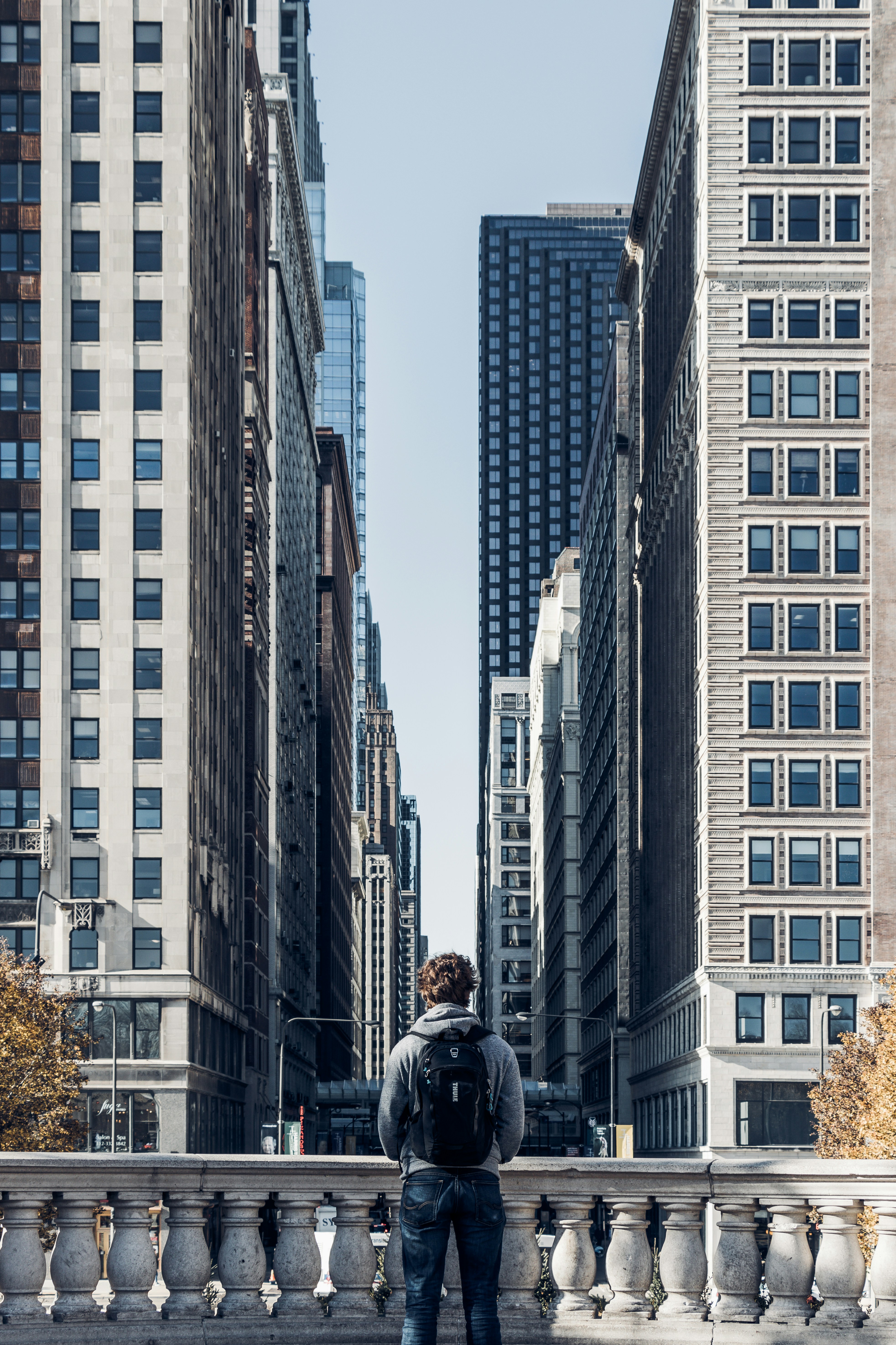 A solitary figure stands at the edge of a grand urban overlook, framed by towering skyscrapers that reflect the modern cityscape's architectural diversity.
