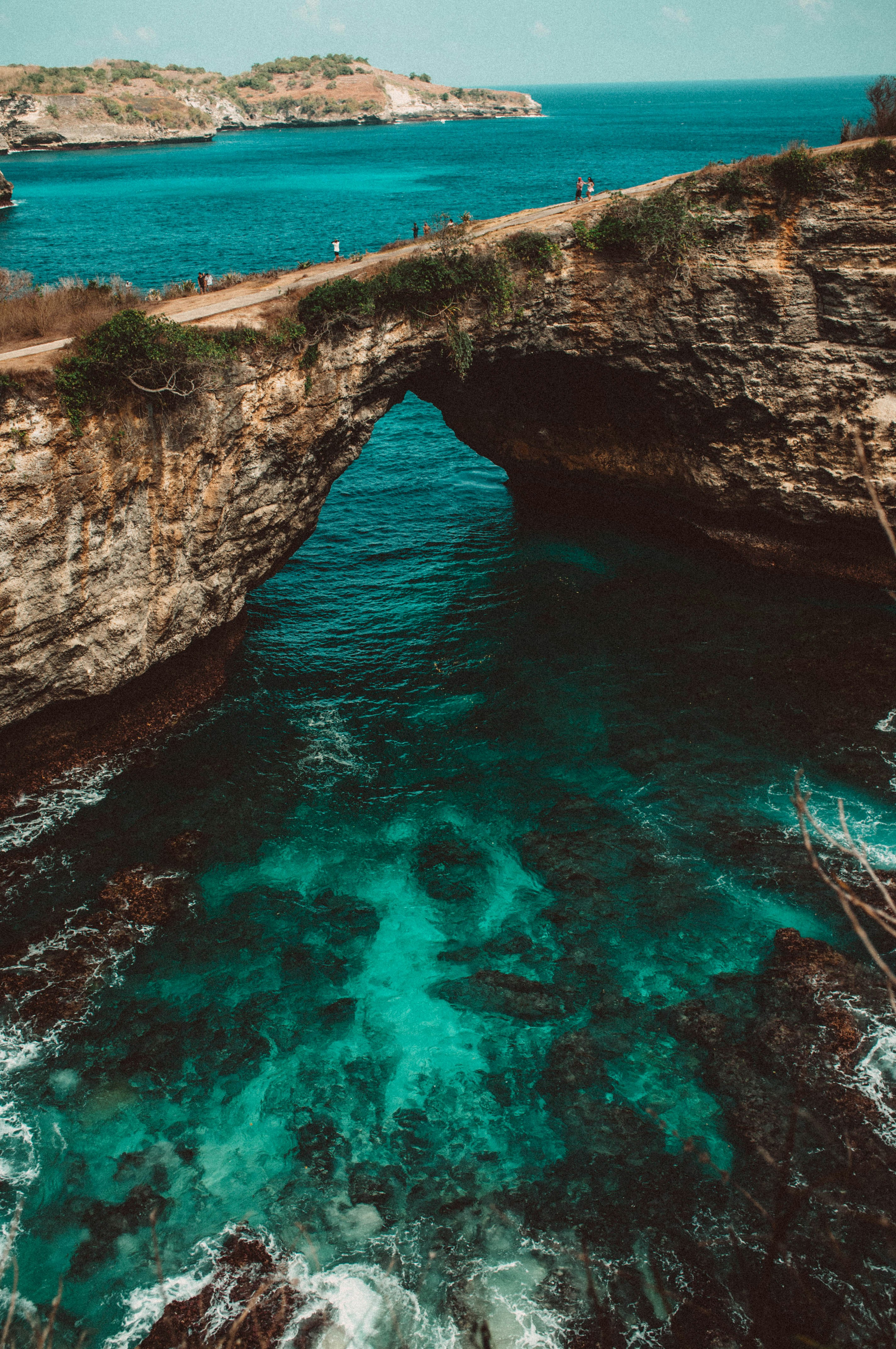 Natural rock arch over a vibrant turquoise sea with rugged cliffs in the background.