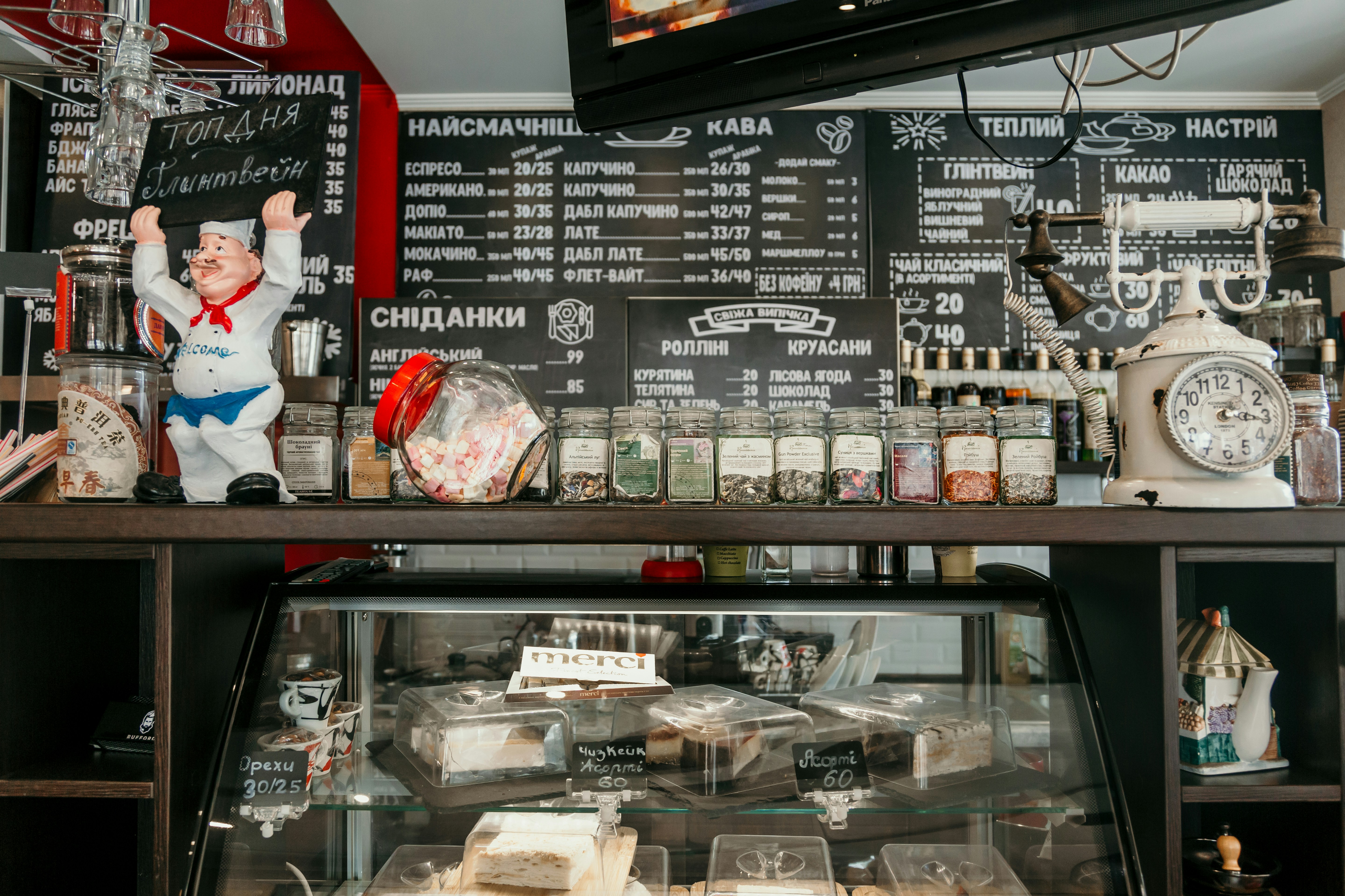 Café counter adorned with retro decor, vintage clock, and a variety of packaged goods under a menu board.