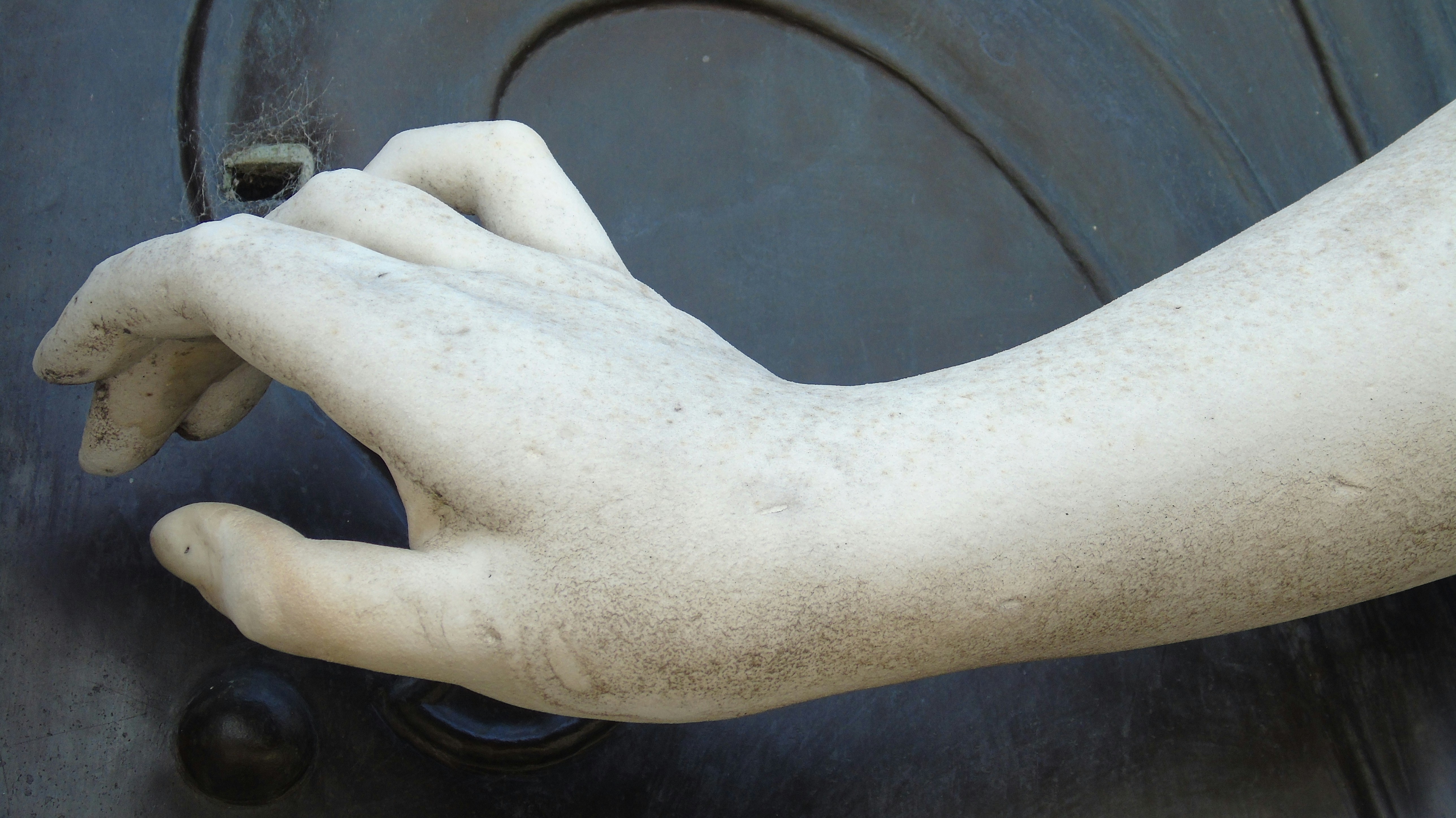 Close-up of a marble hand reaching towards a circular knob on a textured surface, emphasizing intricate details and craftsmanship.