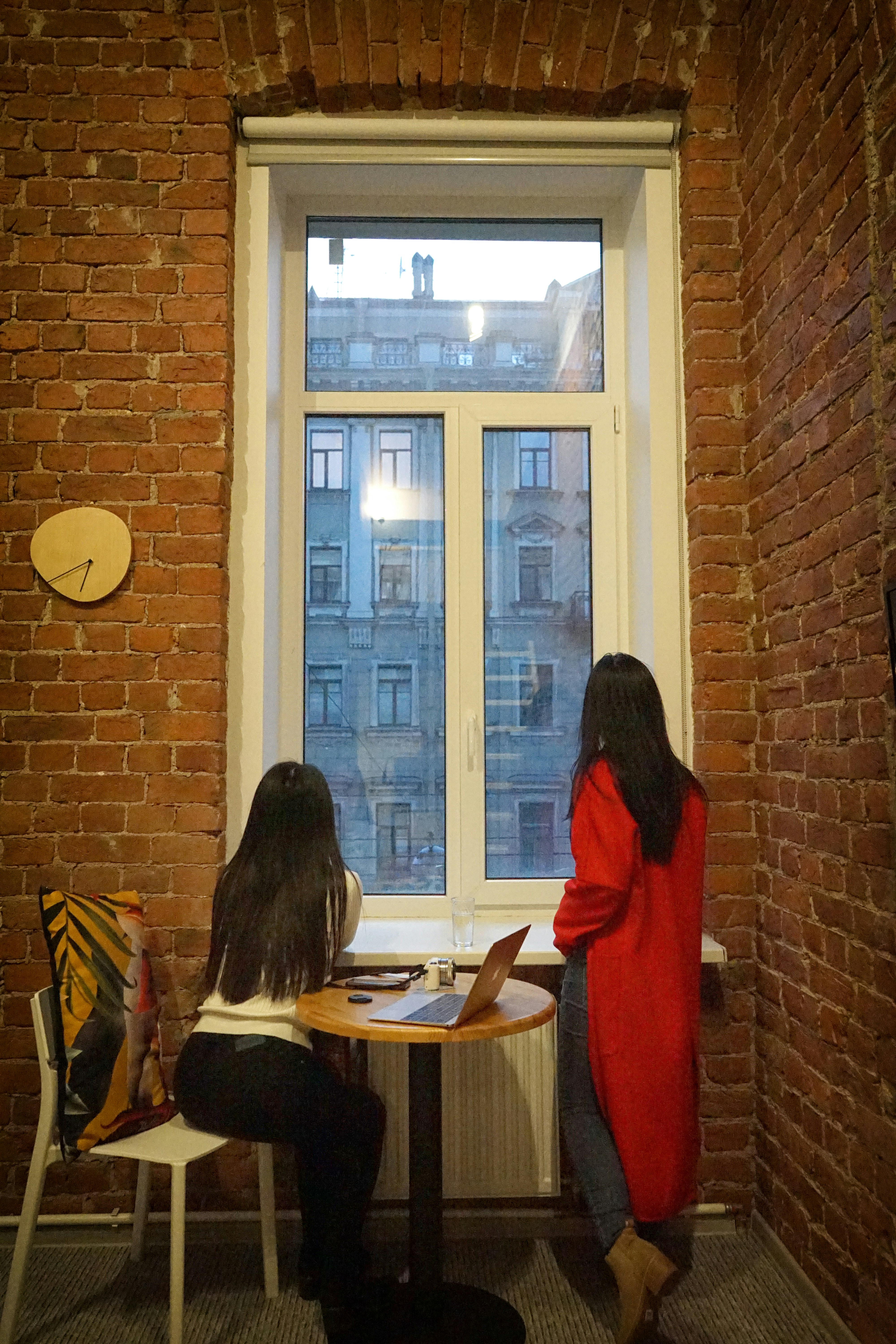 Woman sitting and another woman standing near table while glancing on ...