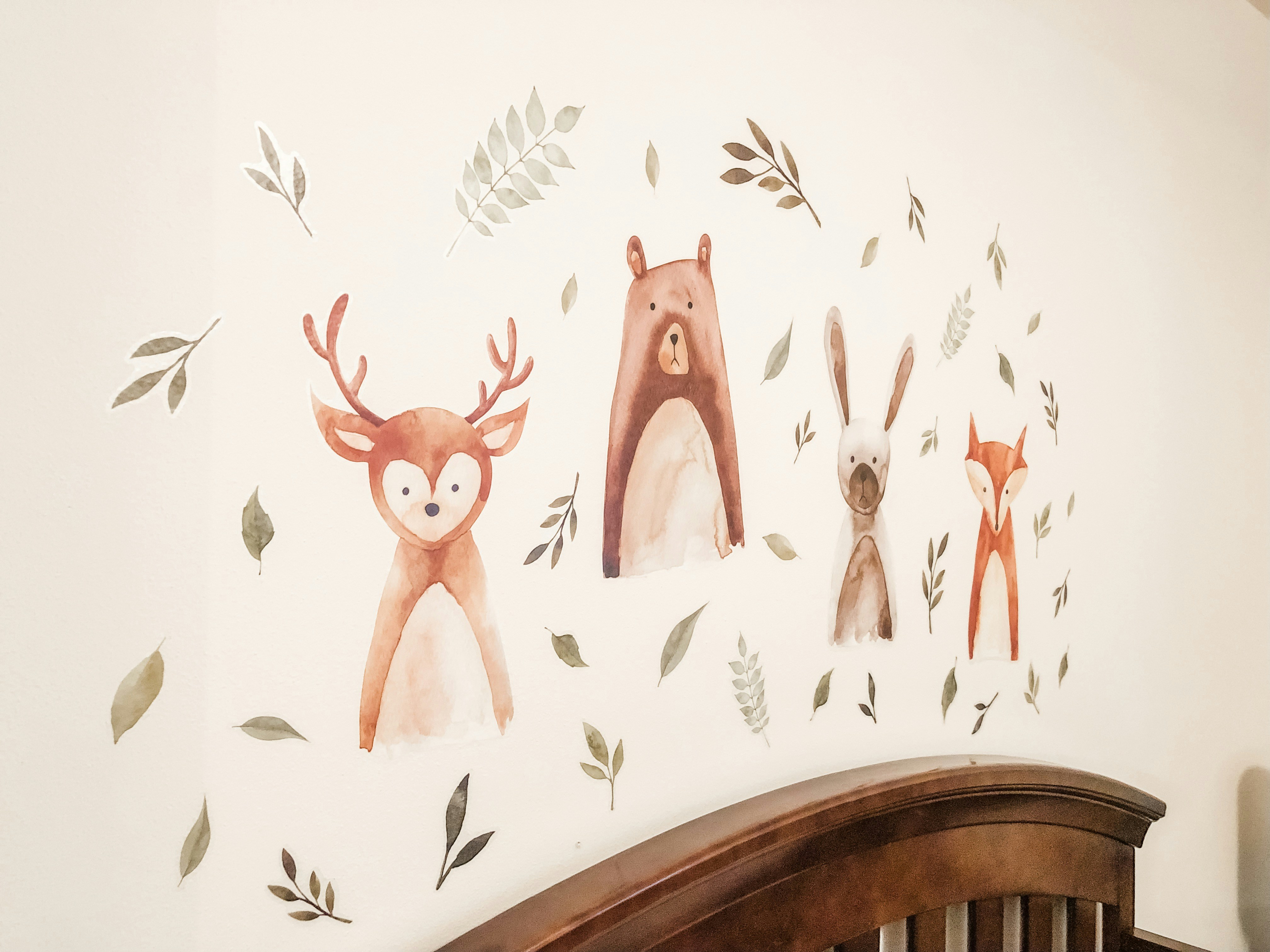 Charming watercolor illustrations of a deer, bear, rabbit, and fox surrounded by delicate leaves on a nursery wall.