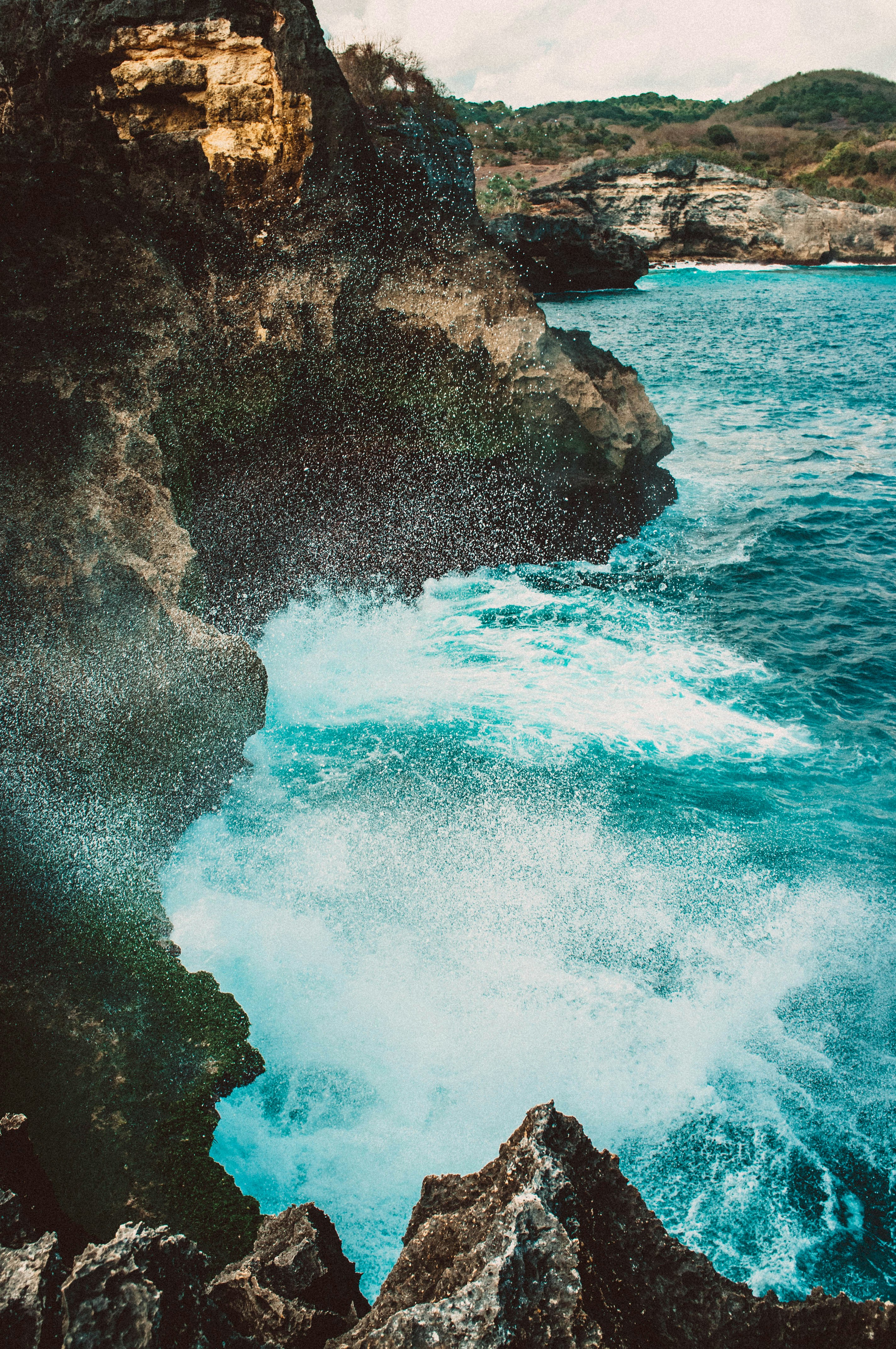 Waves crashing against rocky cliffs, sending sprays of water into the air at a secluded coastal inlet.