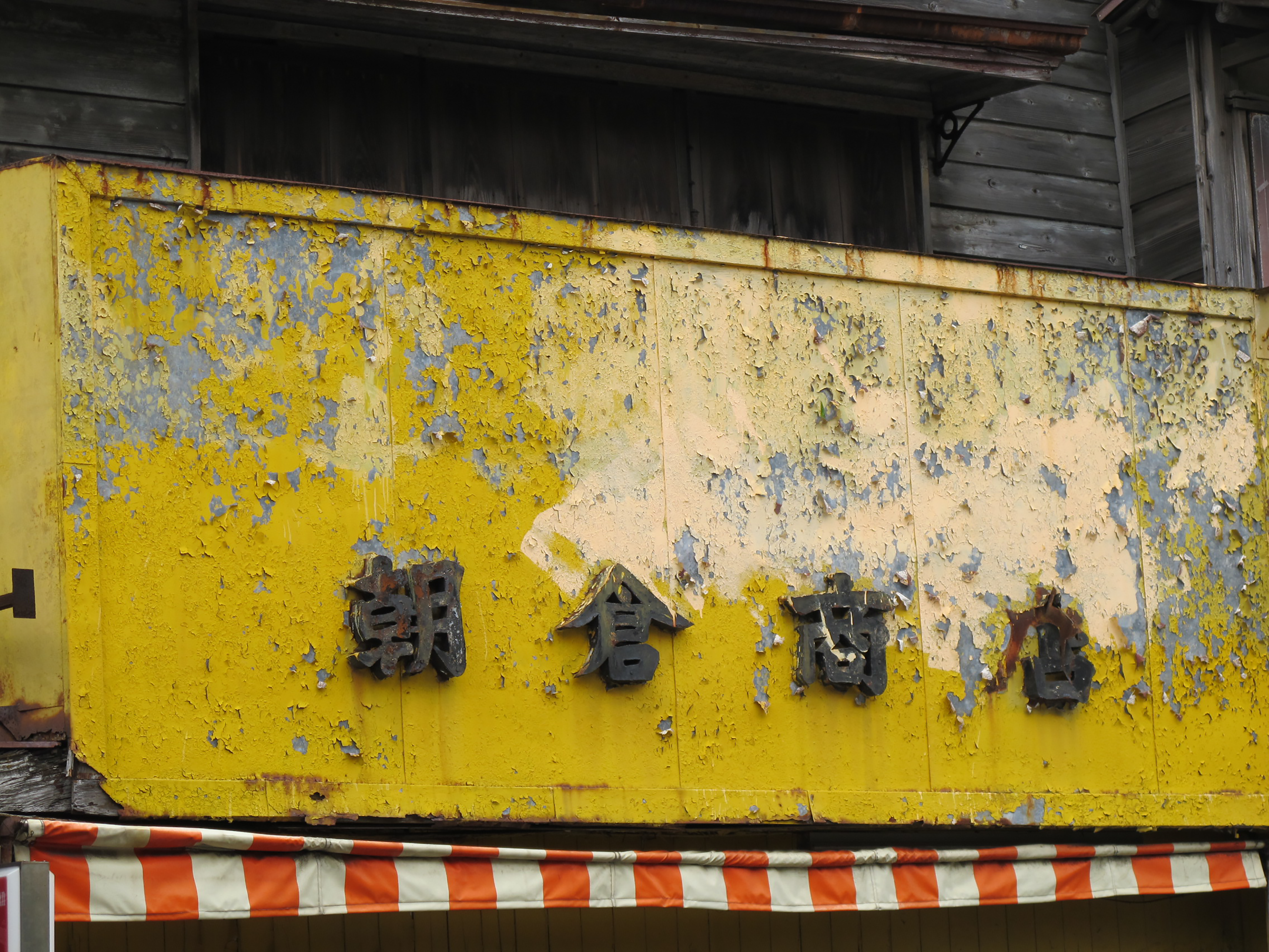 Weathered yellow sign with peeling paint and dark letters, hinting at a once-bustling establishment. A glimpse into urban decay.