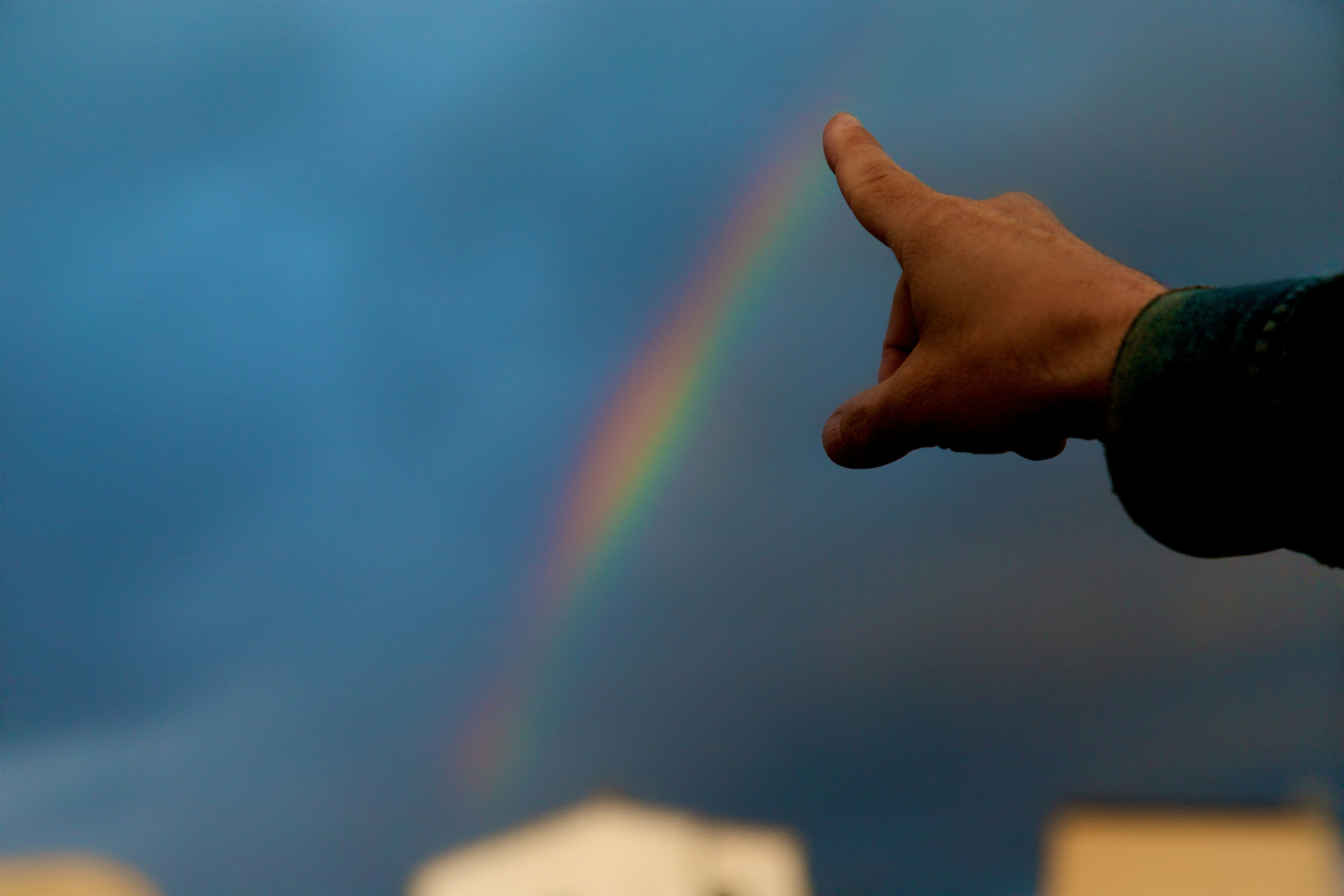 Rainbow Aimed: Hand Reaches Toward the Arc in a Cloudy Sky