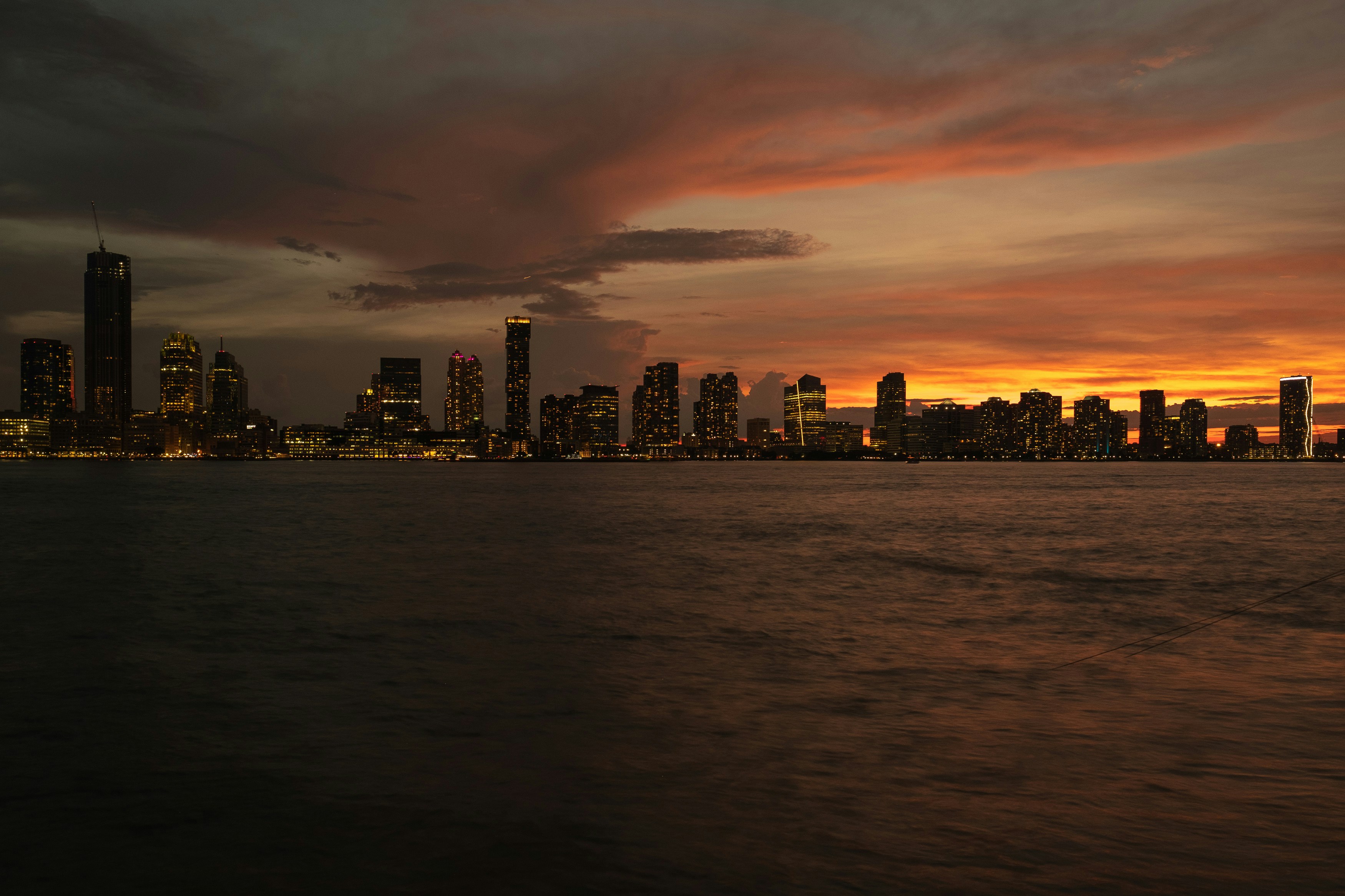 City skyline silhouetted against a vibrant sunset sky over calm waters.