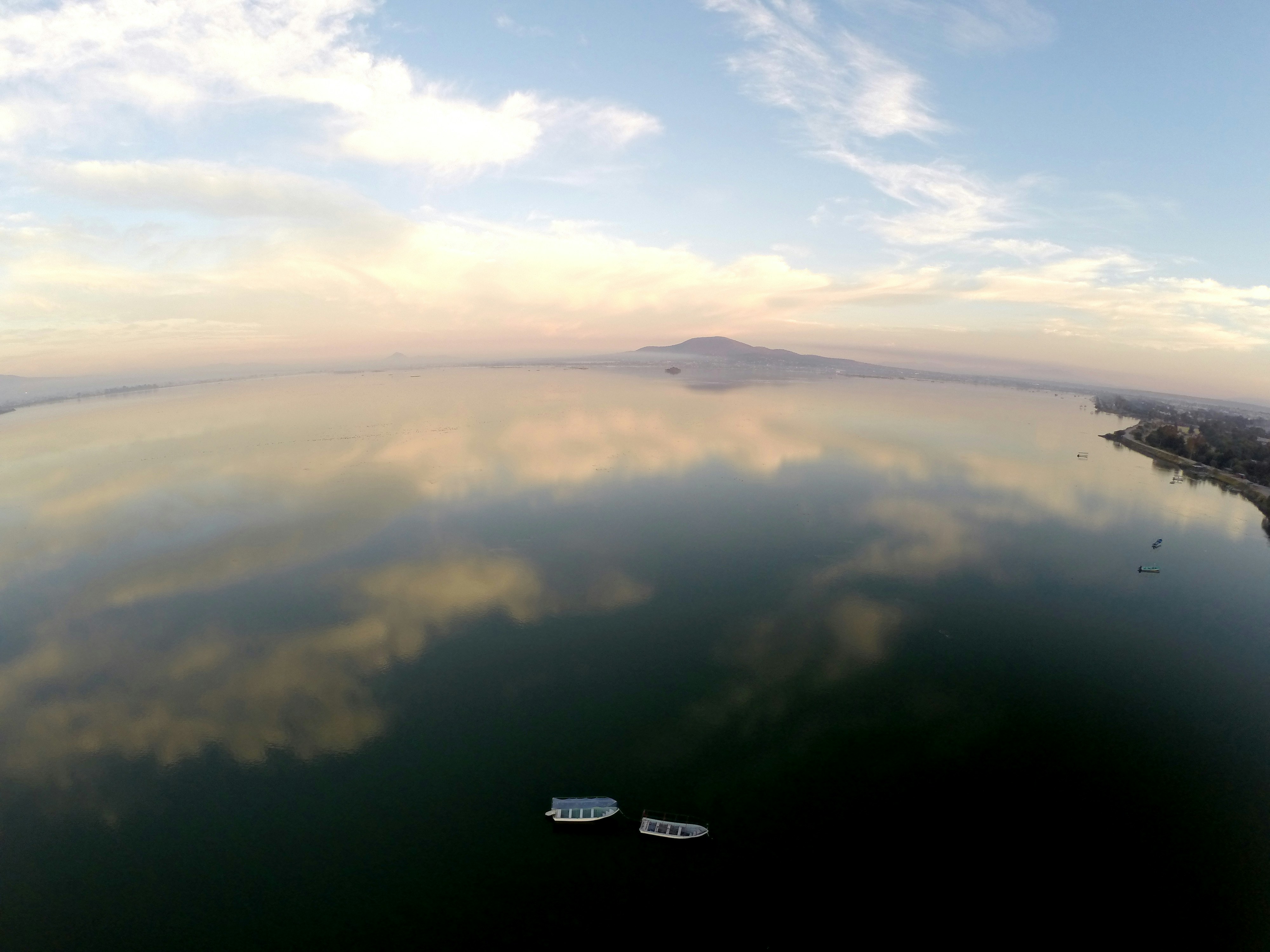 Expansive lake reflecting soft clouds and distant mountains at dusk.