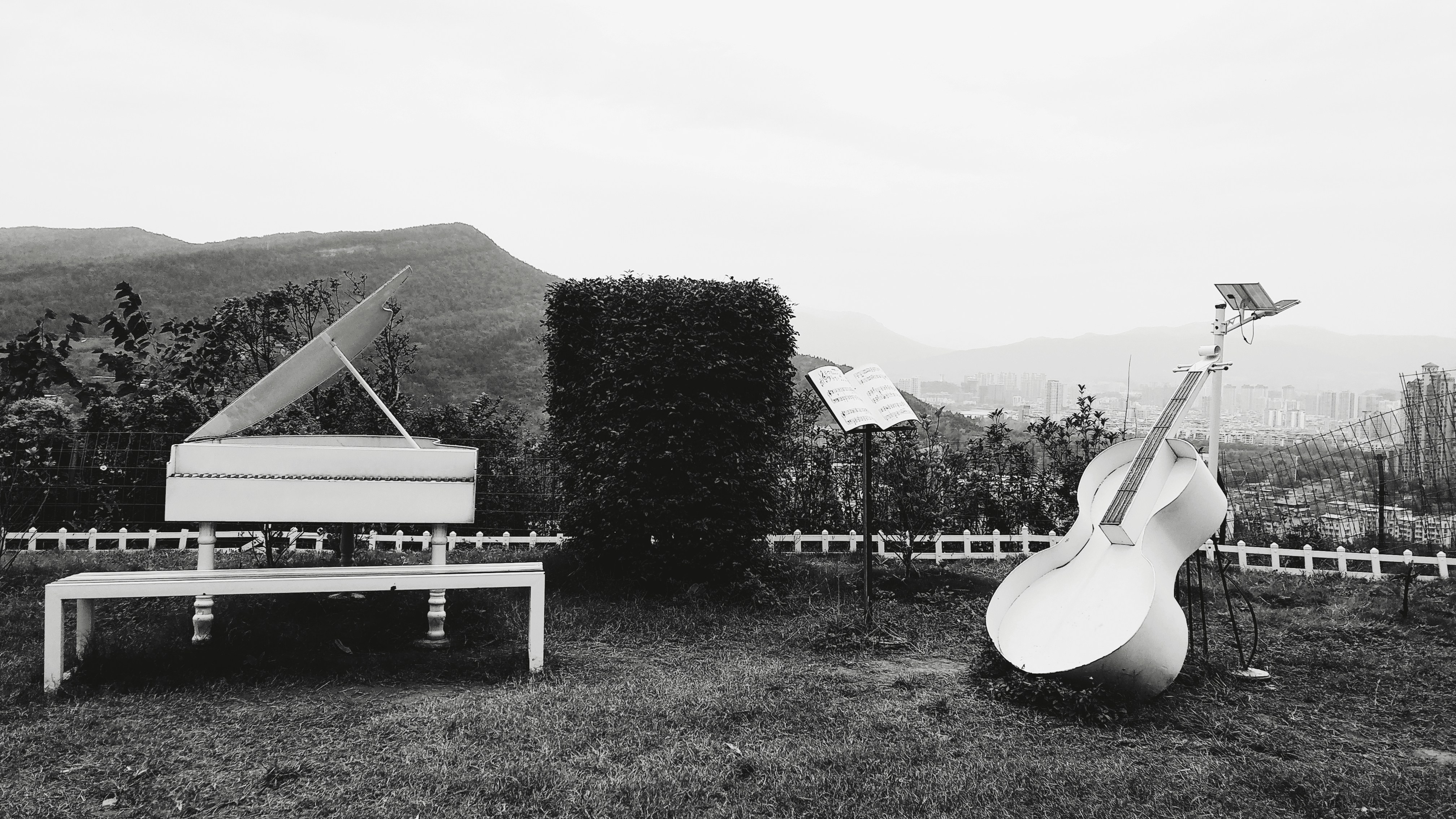 A grand piano and a large guitar sculpture set against a mountainous backdrop, creating a serene musical atmosphere. Sheet music stands nearby, inviting a sense of artistic expression.