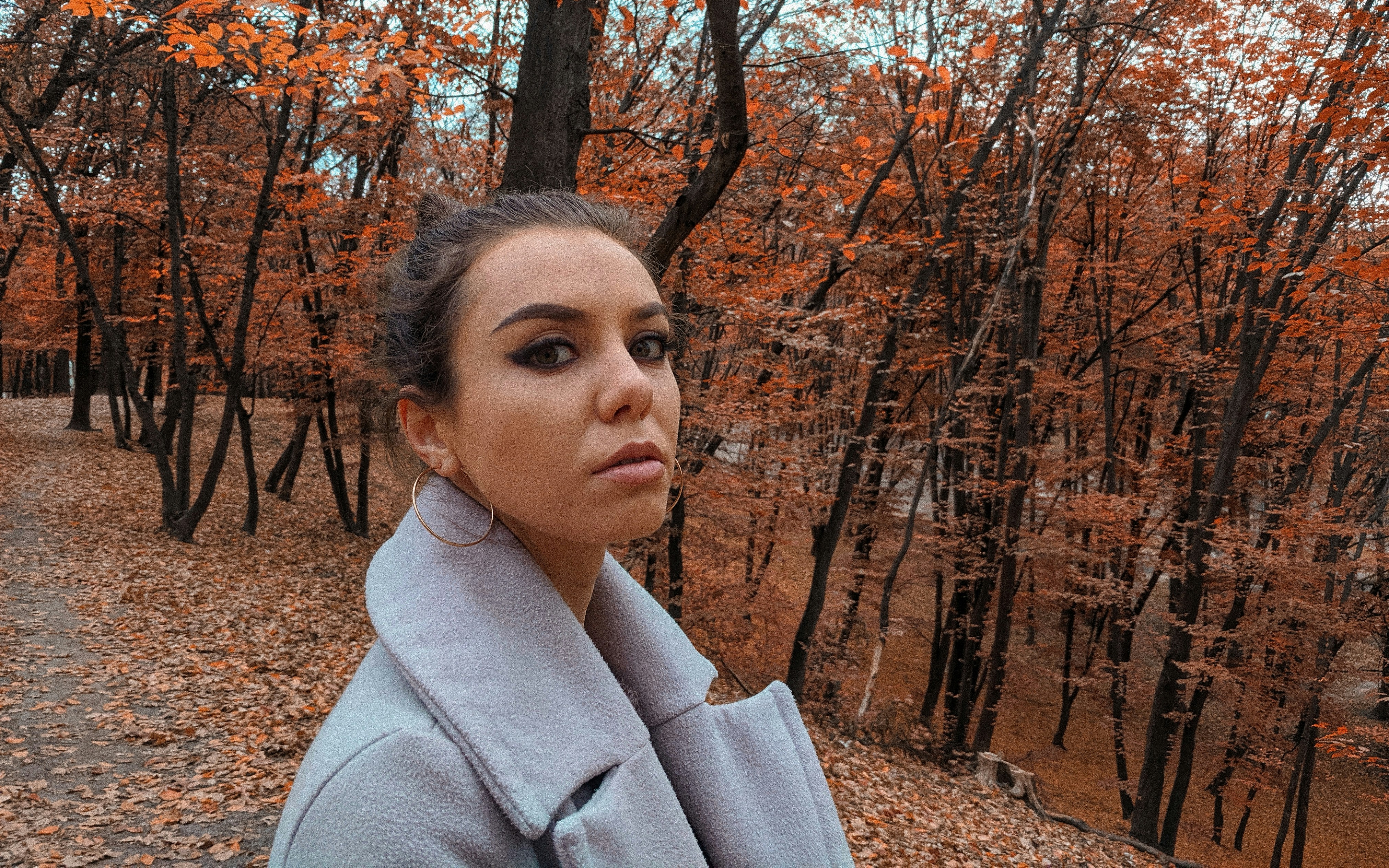 Young woman gazing thoughtfully amidst a forest of vibrant autumn foliage. The scene captures the essence of fall with rich, warm colors.