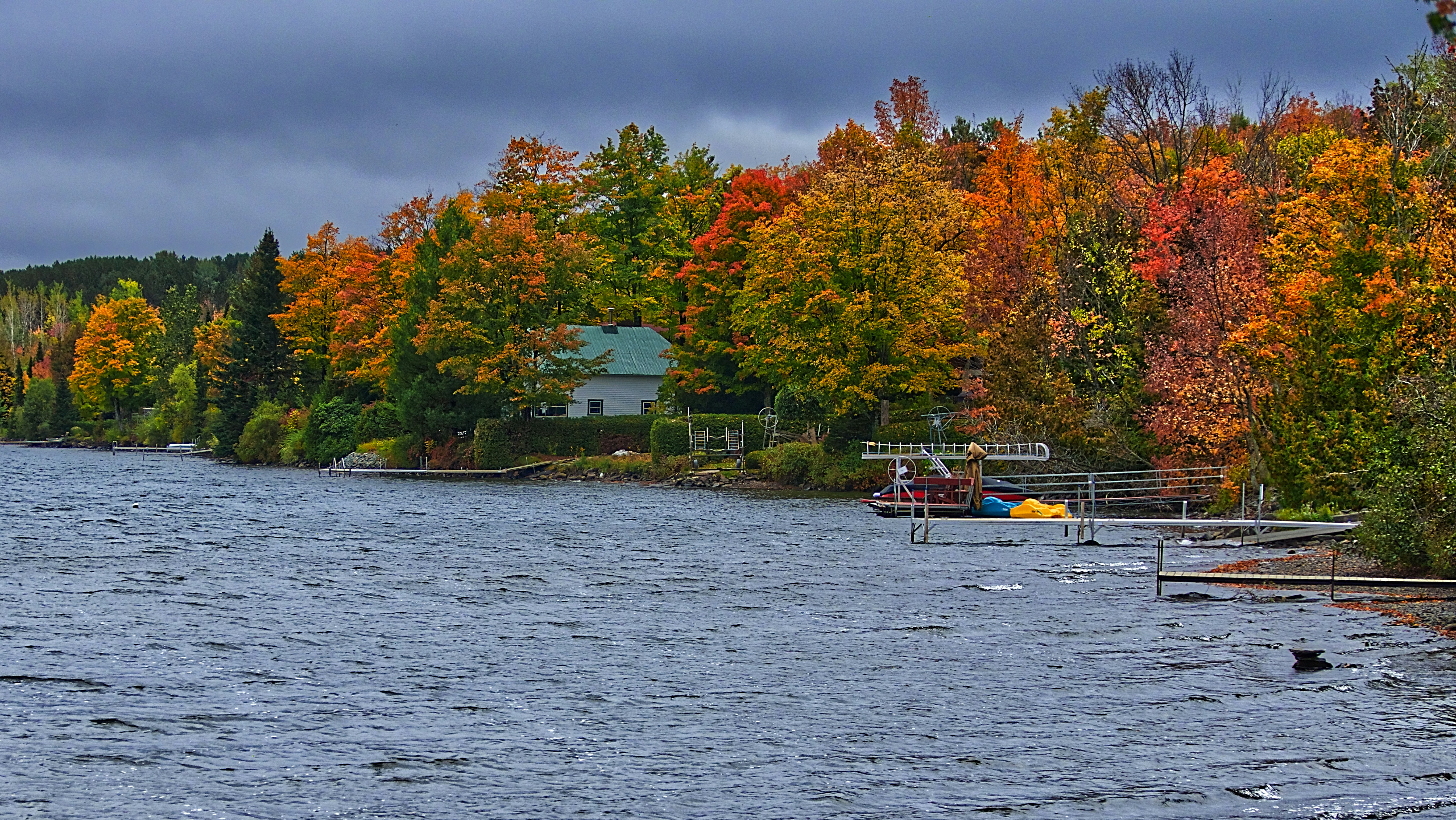 Vibrant autumn foliage reflecting on a tranquil lake, with a cozy house nestled among the trees. The scene captures the essence of fall's transition.