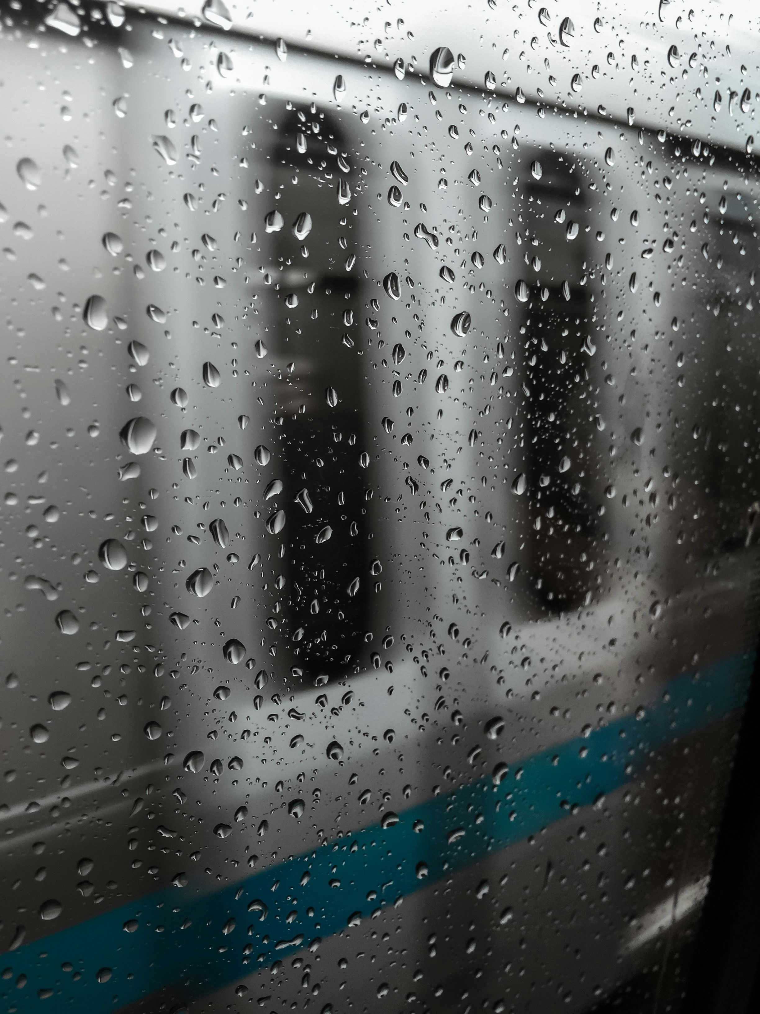 Beads on Glass: Rain-Kissed Window with a Teal-Striped Train in Soft Focus