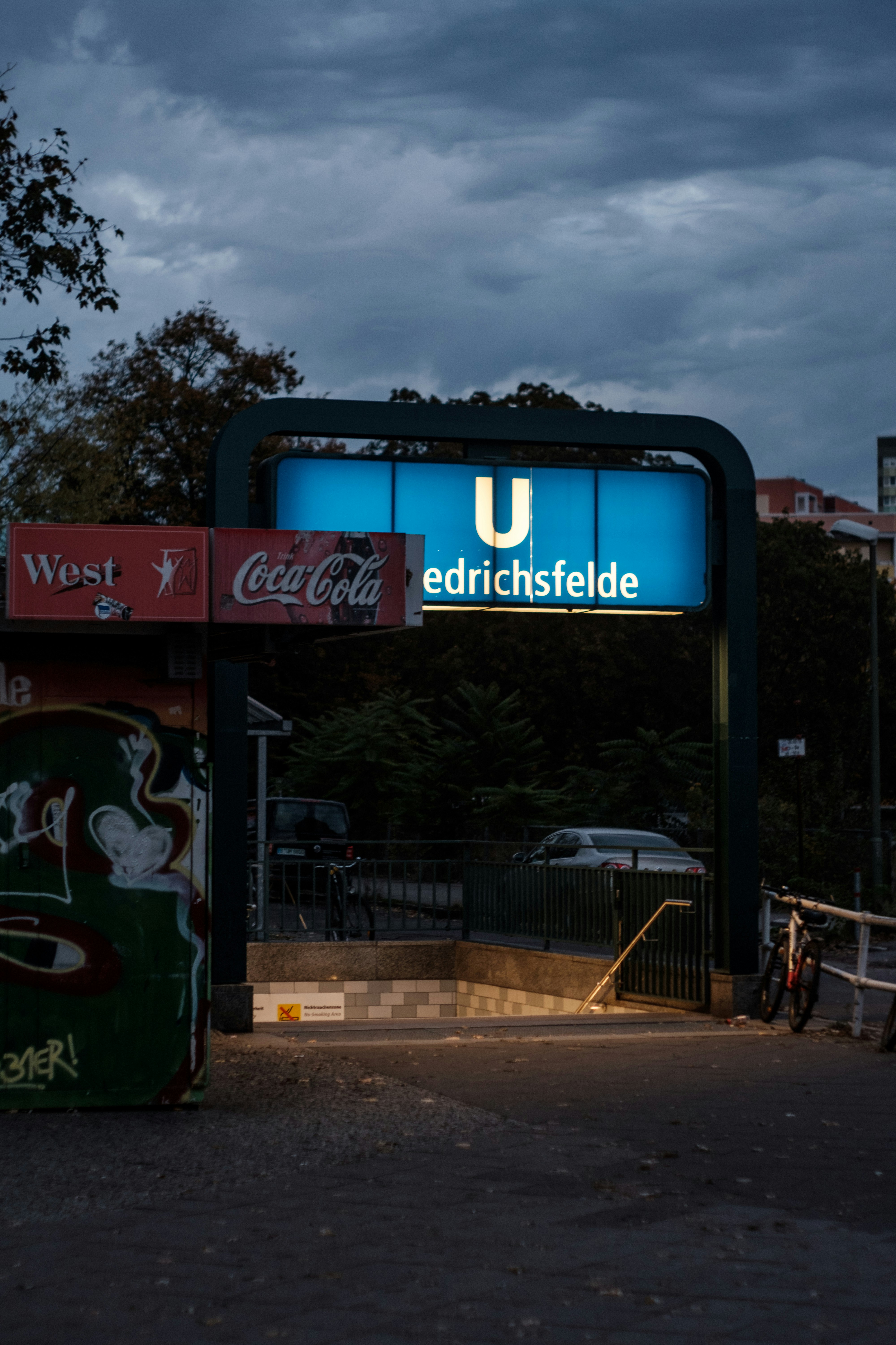Illuminated subway entrance sign at Edrichsfelde, framed by evening shadows and urban surroundings.