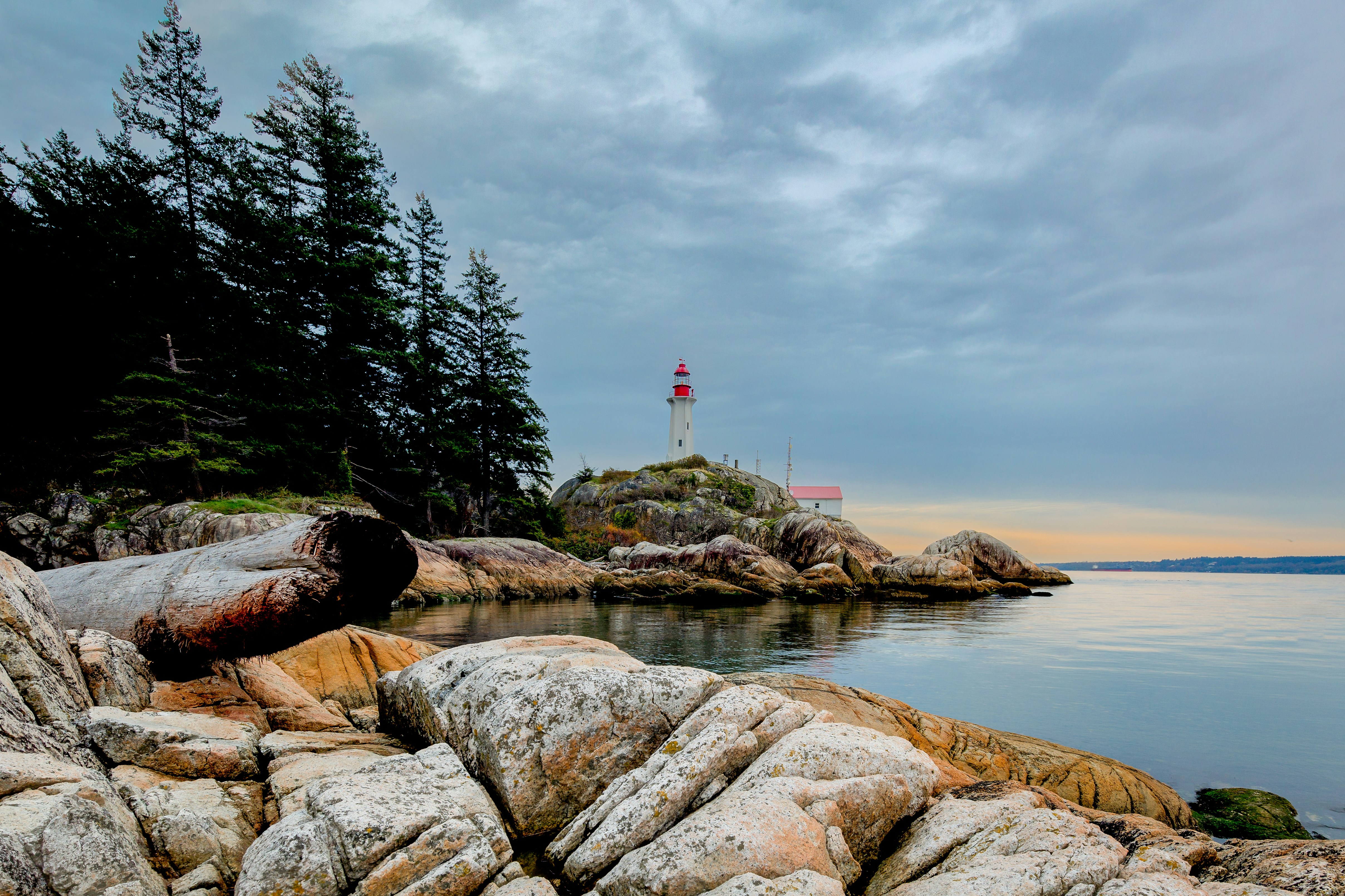 Lighthouse perched on rocky outcrop, surrounded by calm waters and evergreen trees, reflecting the soft hues of dawn.