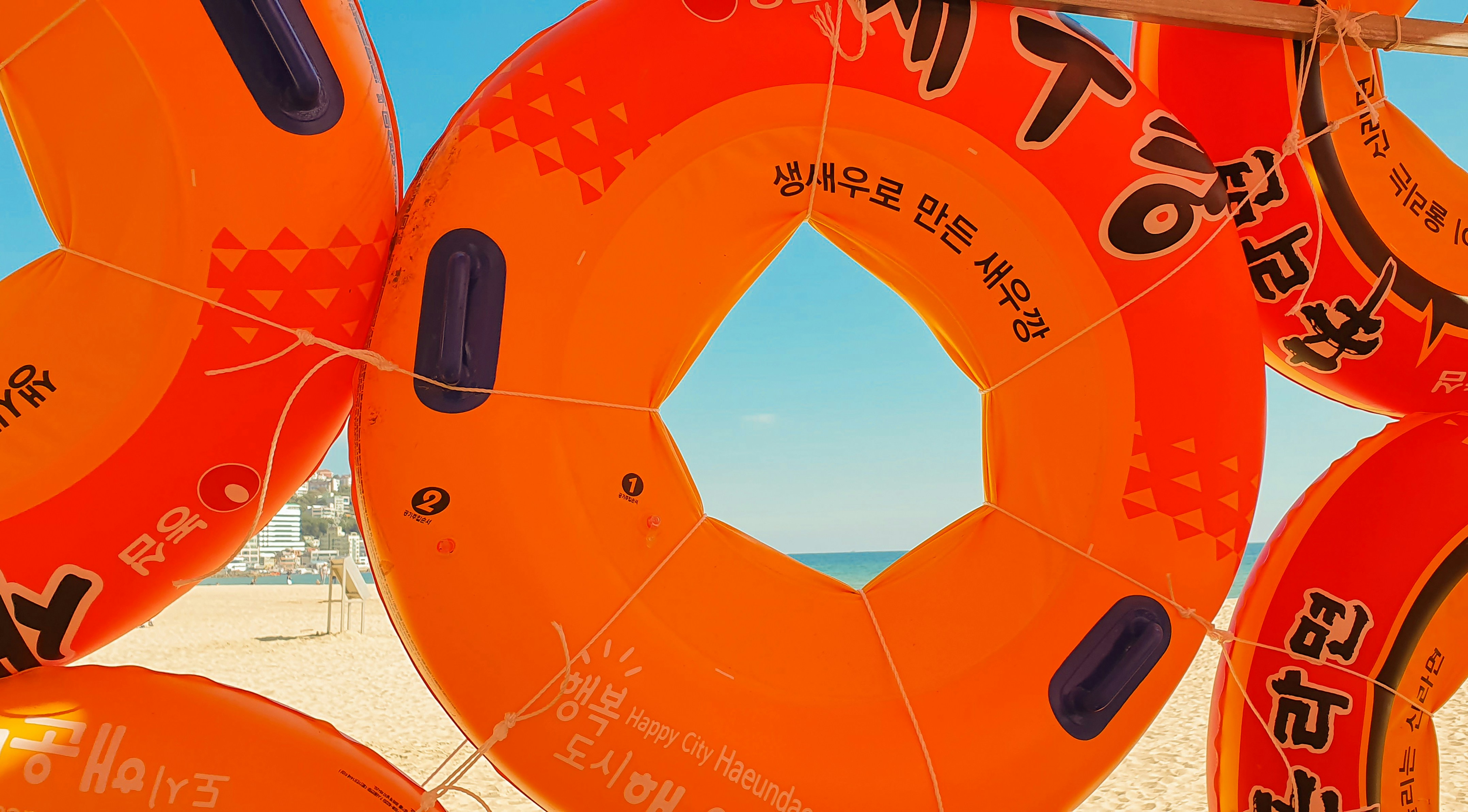 Lifebuoy Window: Neon Orange Rings Framing a Sunlit Beach