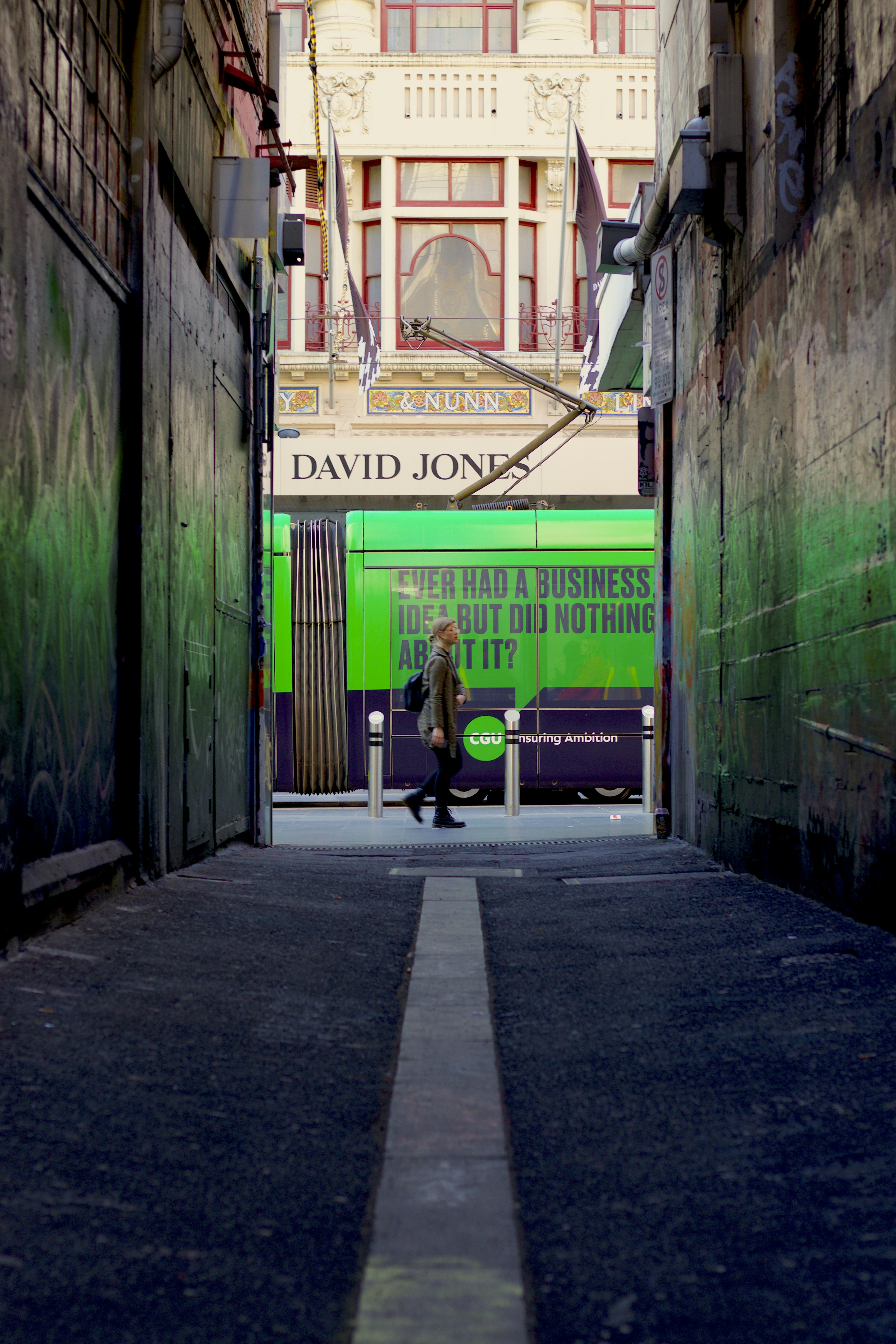 A pedestrian walks through a narrow alley, framed by colorful graffiti, with a bus displaying an intriguing advertisement in the background.