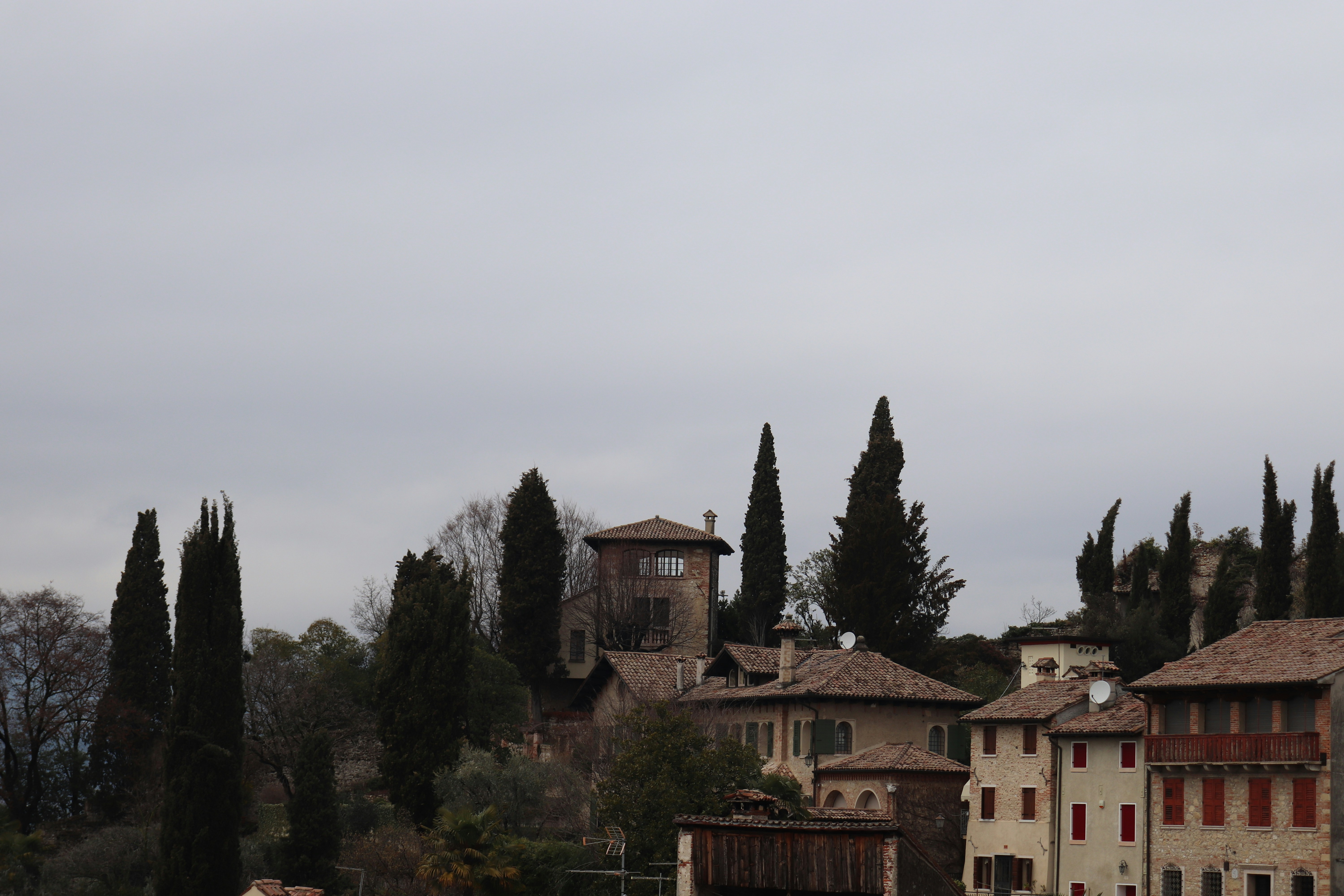 Historic village nestled among cypress trees, showcasing rustic architecture and a moody sky.