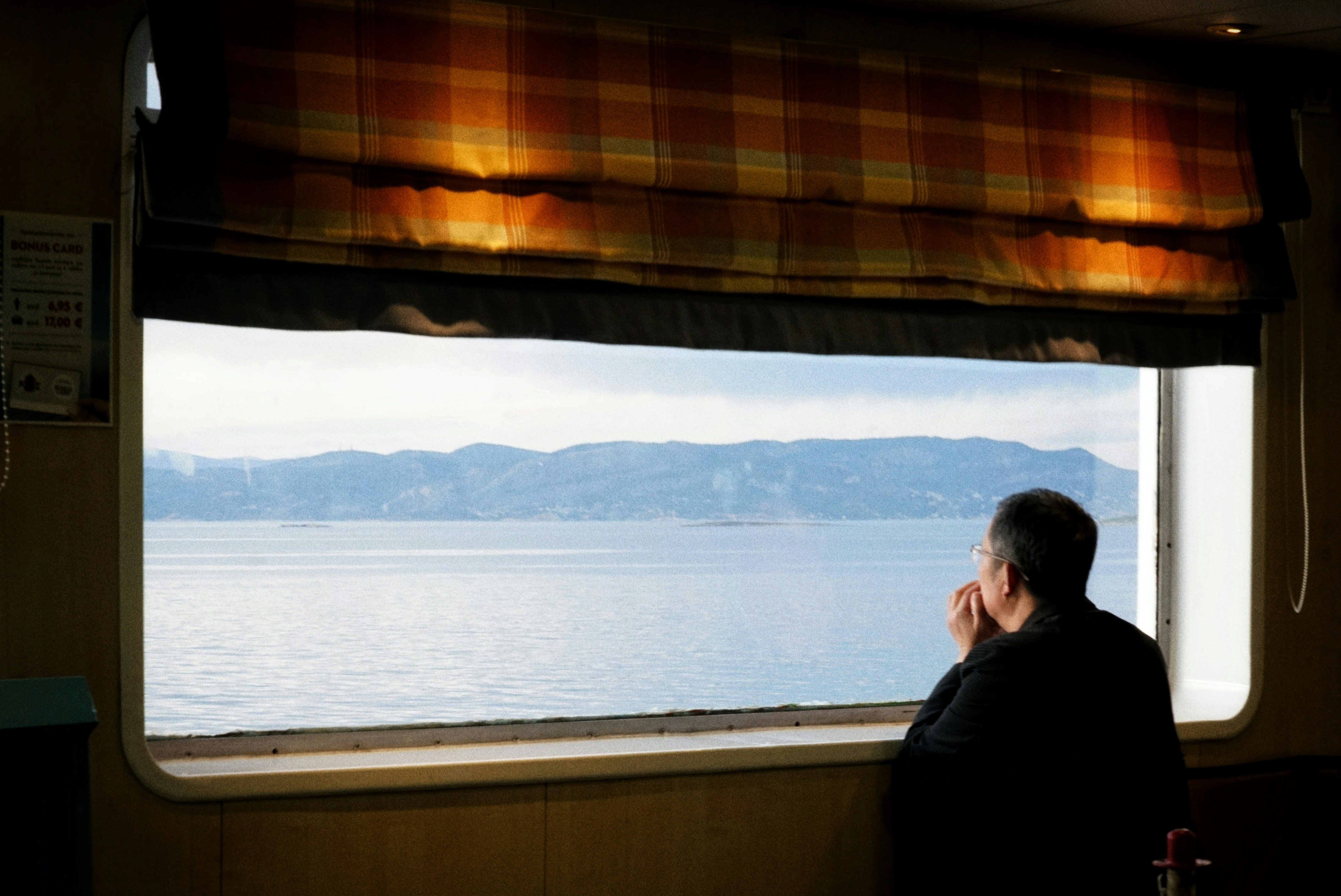 Man standing by glass window facing a calm sea during daytime photo ...