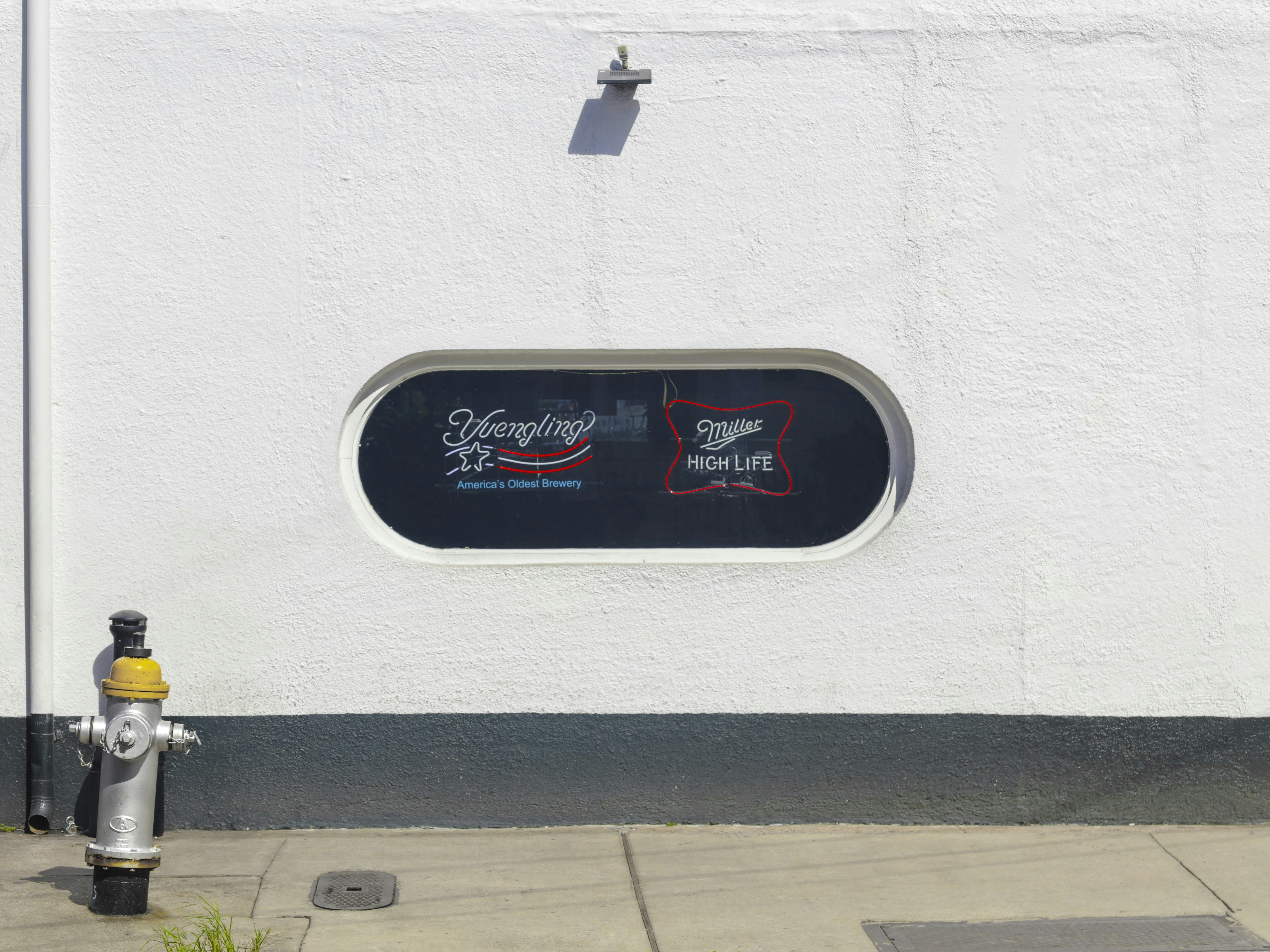 Oval Window on a White Wall: Retro Beer Logos Framed by a Solitary Hydrant