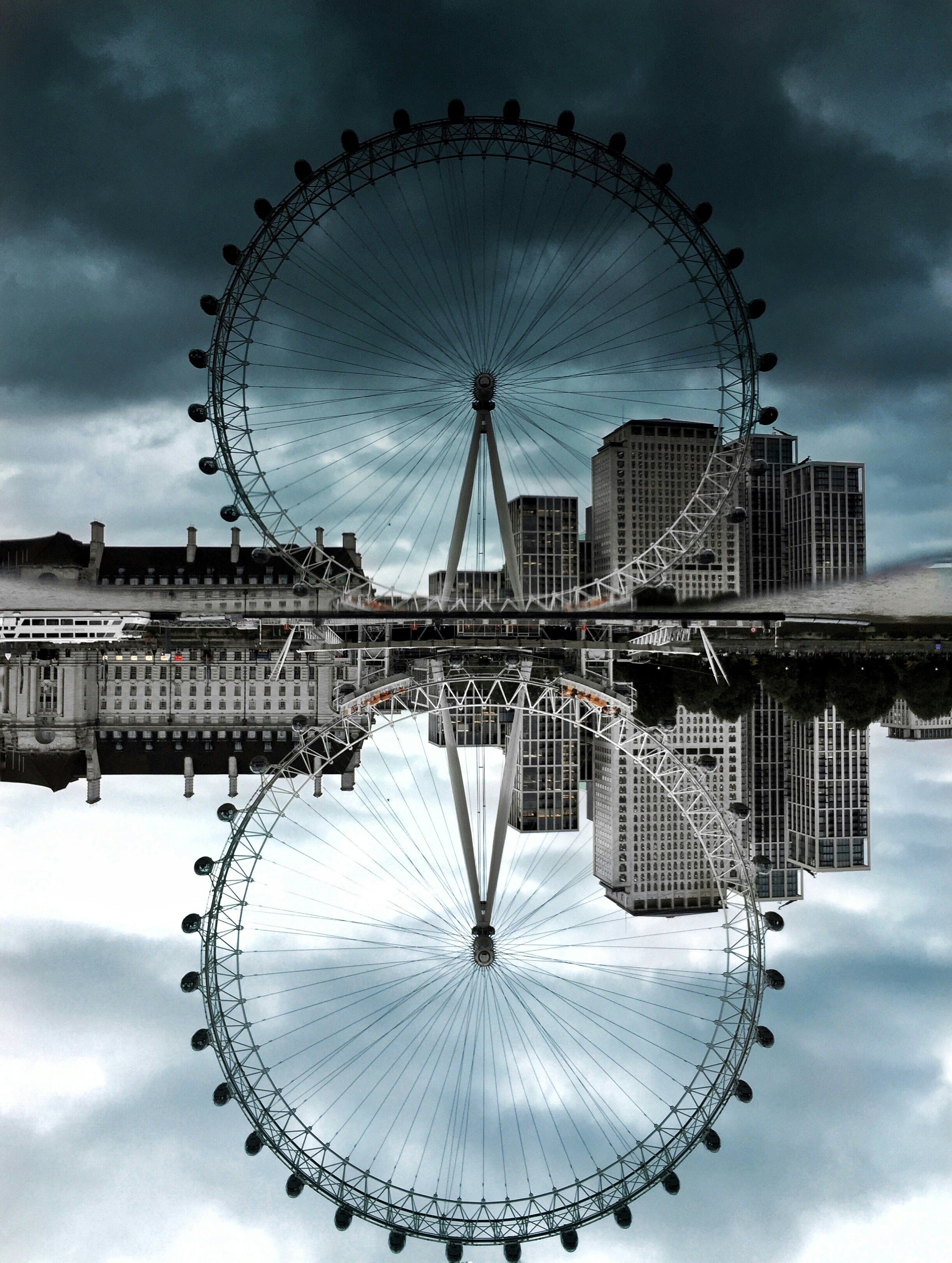 A Ferris wheel mirrored in a calm body of water under a dramatic sky, showcasing urban architecture in the background.
