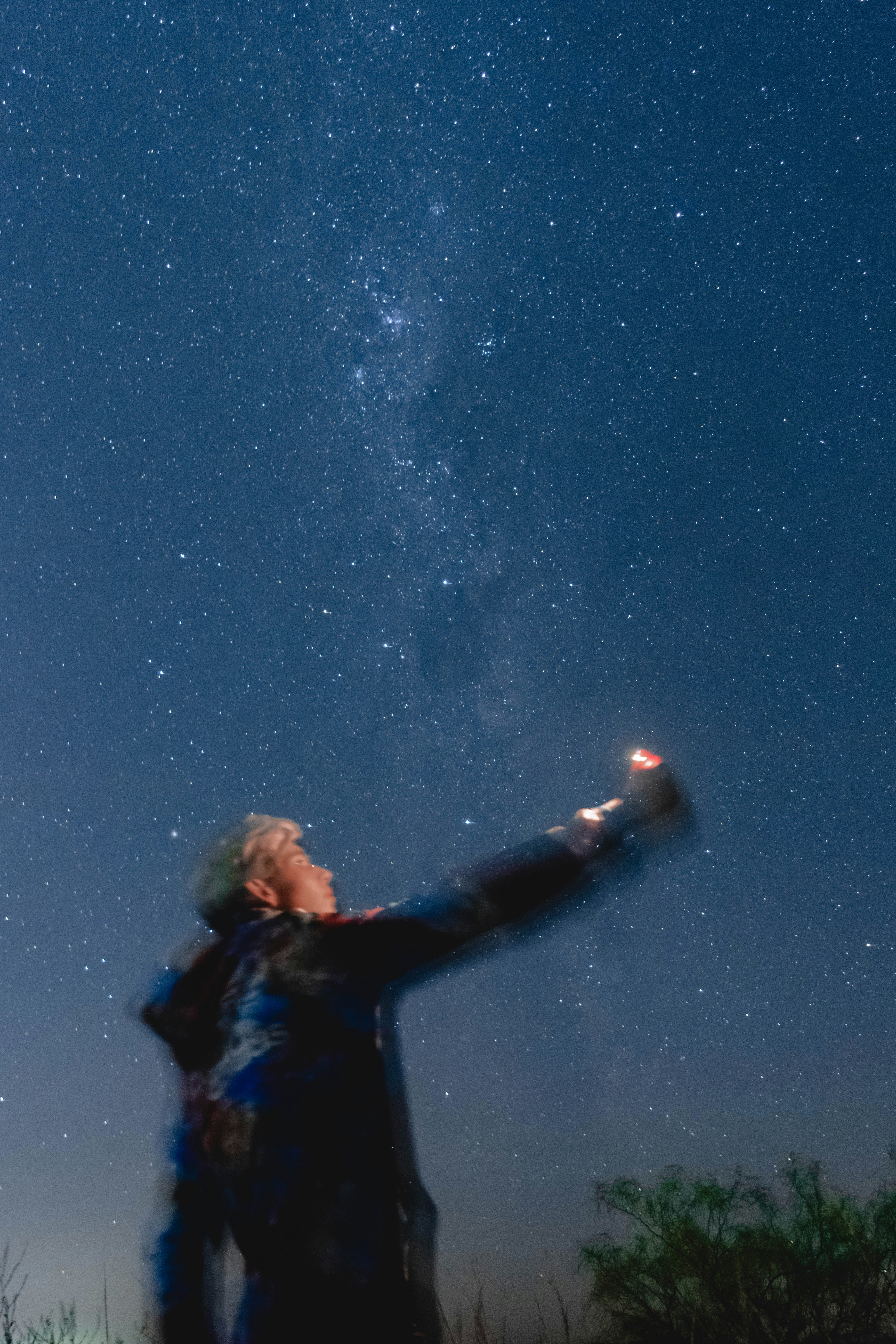 Person pointing a flashlight towards the starry sky, surrounded by a vast expanse of stars and the Milky Way galaxy.