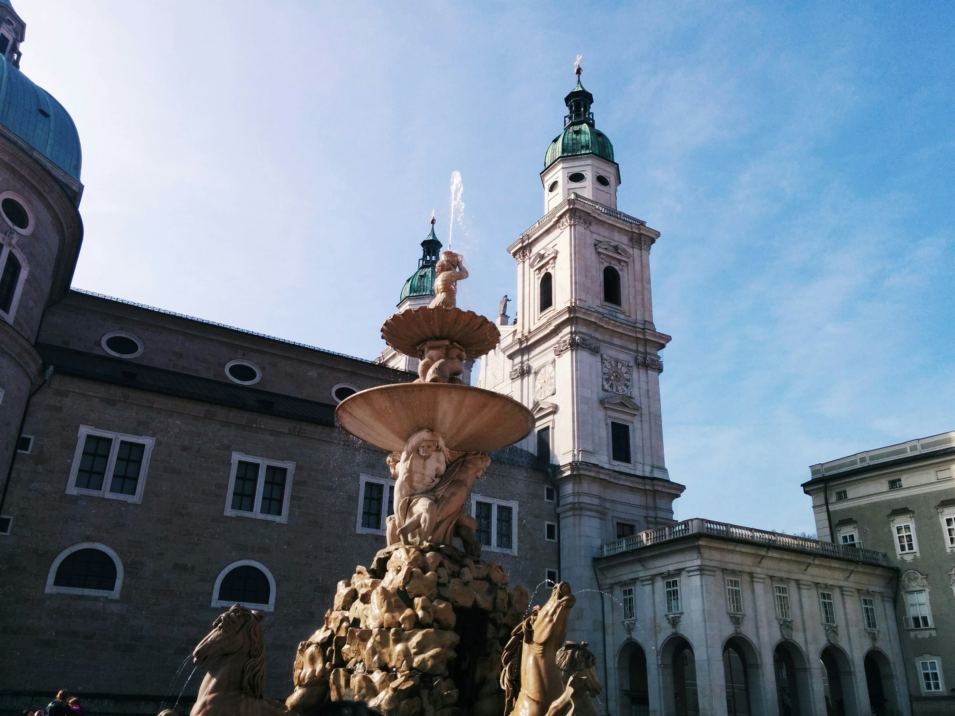 Ornate fountain adorned with sculptures, set against a backdrop of historic architecture under a clear blue sky.