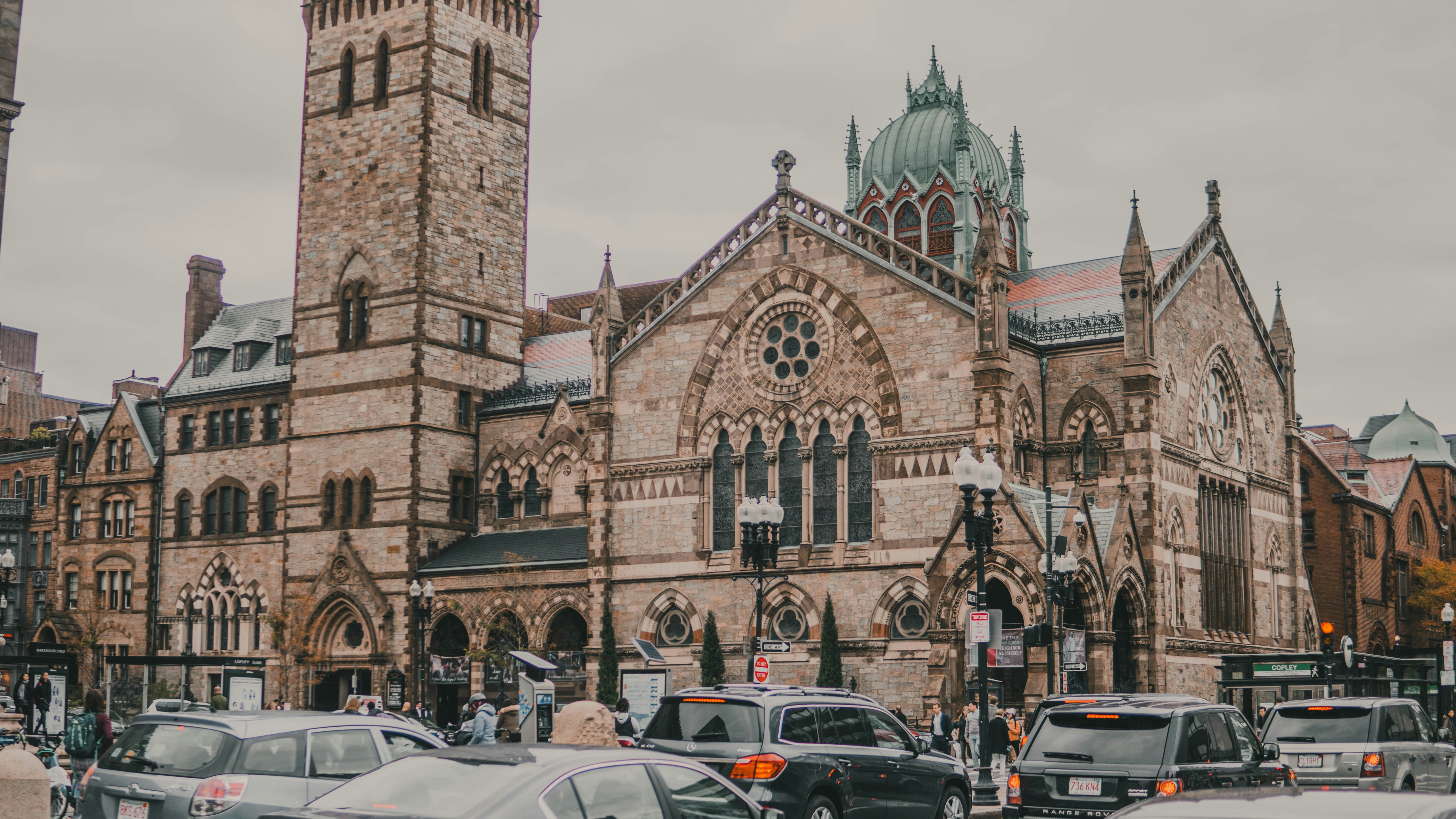 Gothic-style building with intricate stonework surrounded by urban traffic and overcast skies.