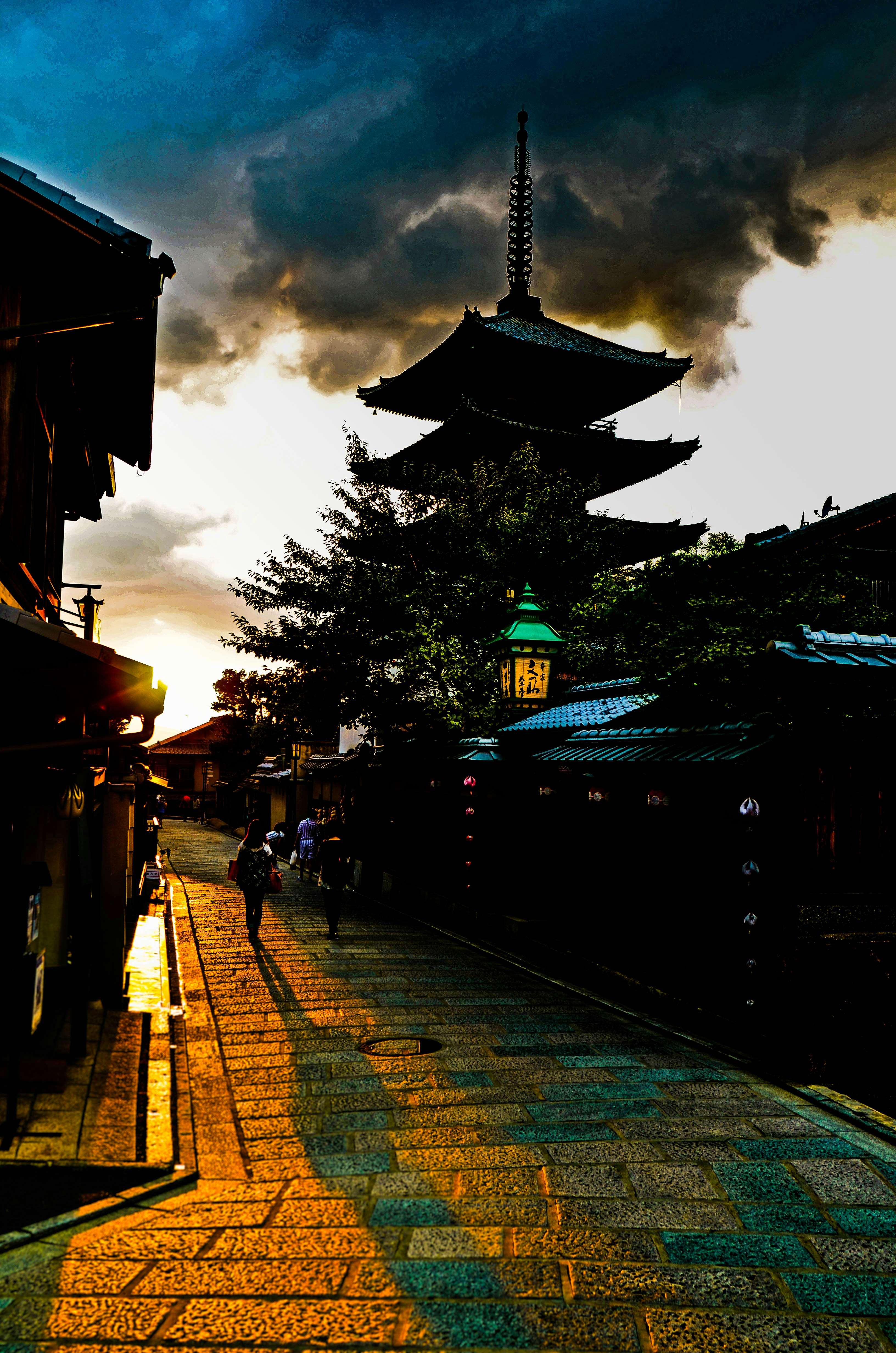 Pagoda silhouetted against a dramatic sky at sunset on a cobblestone street.