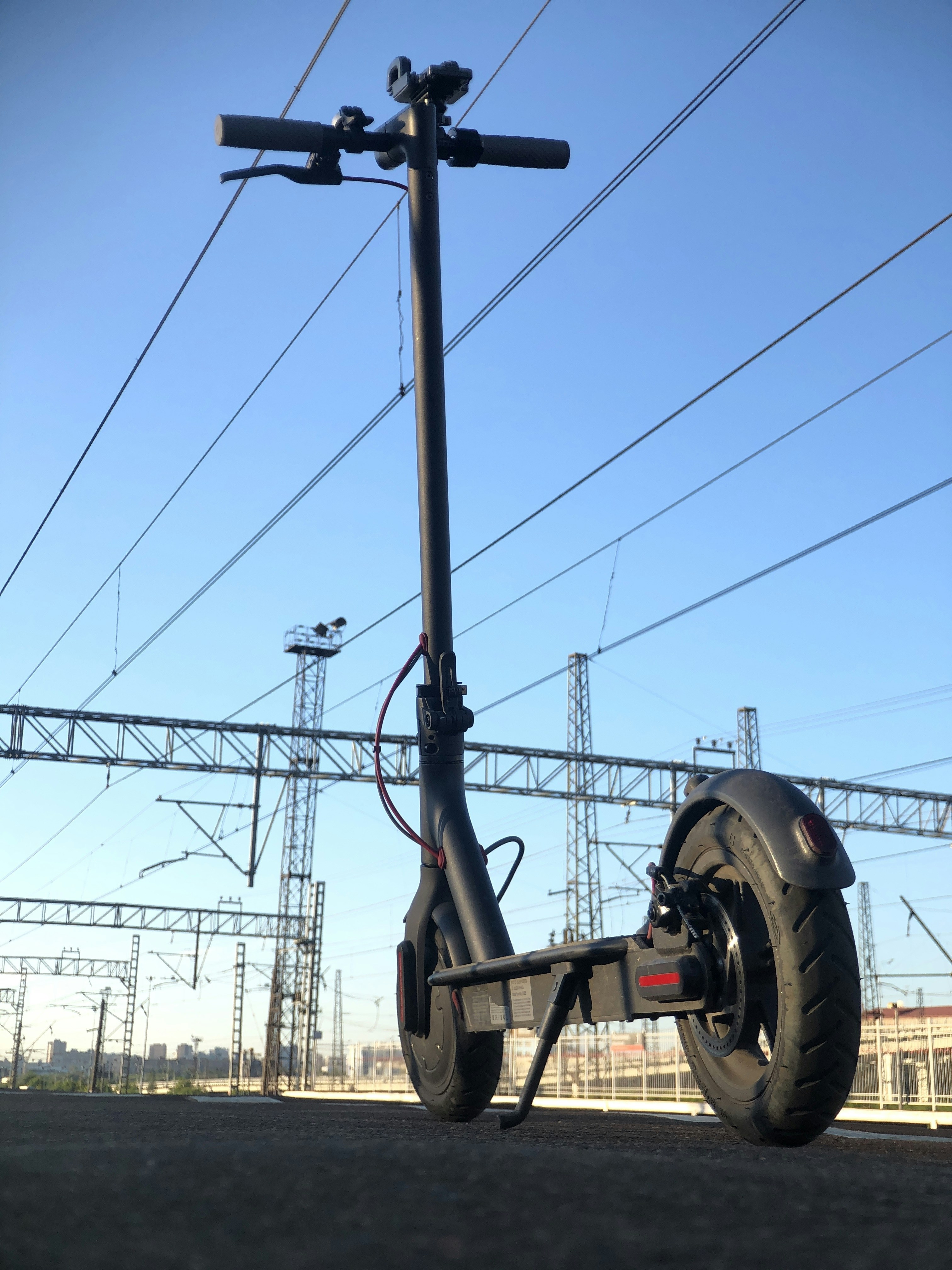 Low-angle portrait of a lone electric scooter framed by railway infrastructure under a clear blue sky
