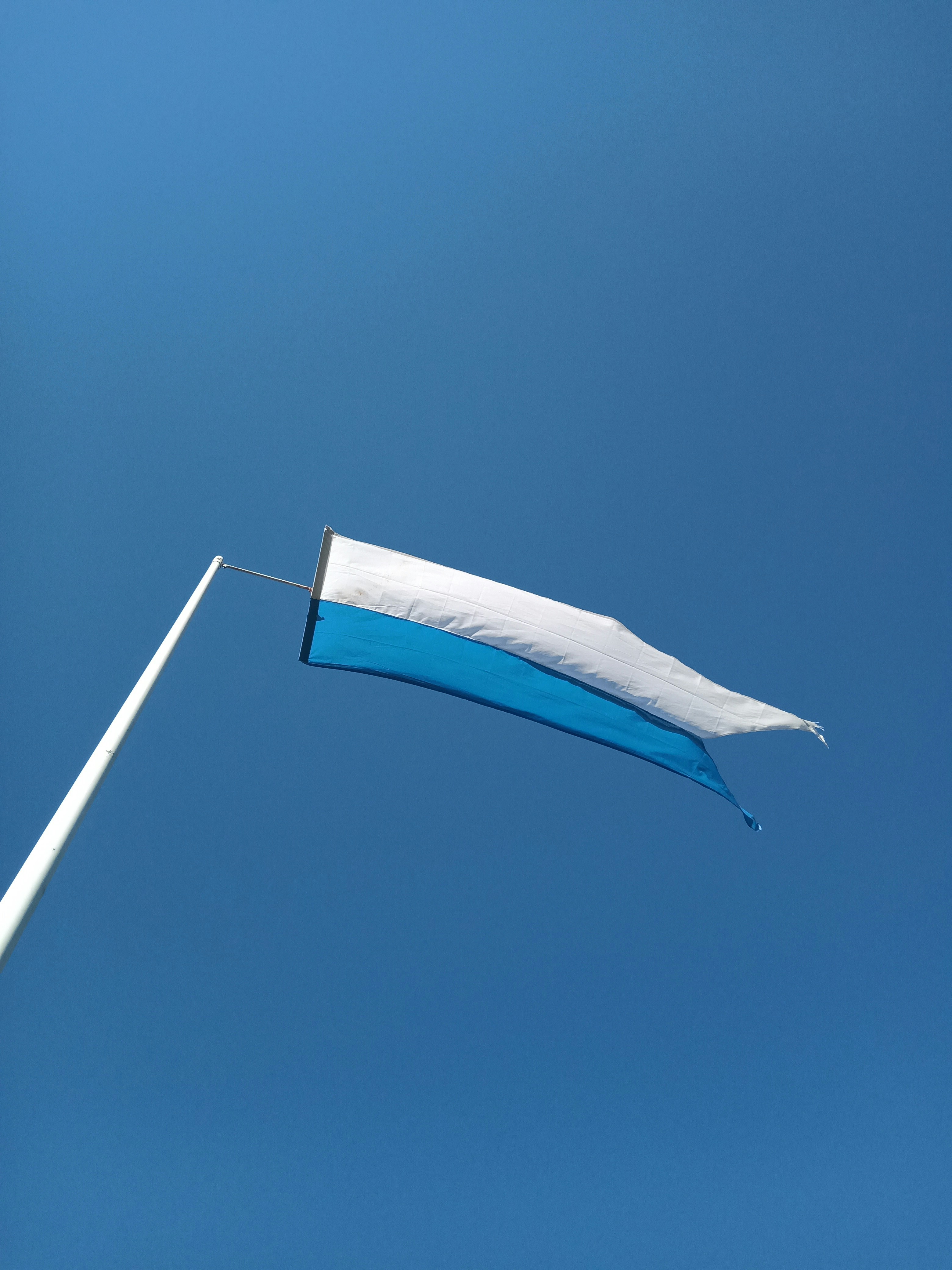 A flag with blue and white sections fluttering against a clear blue sky.