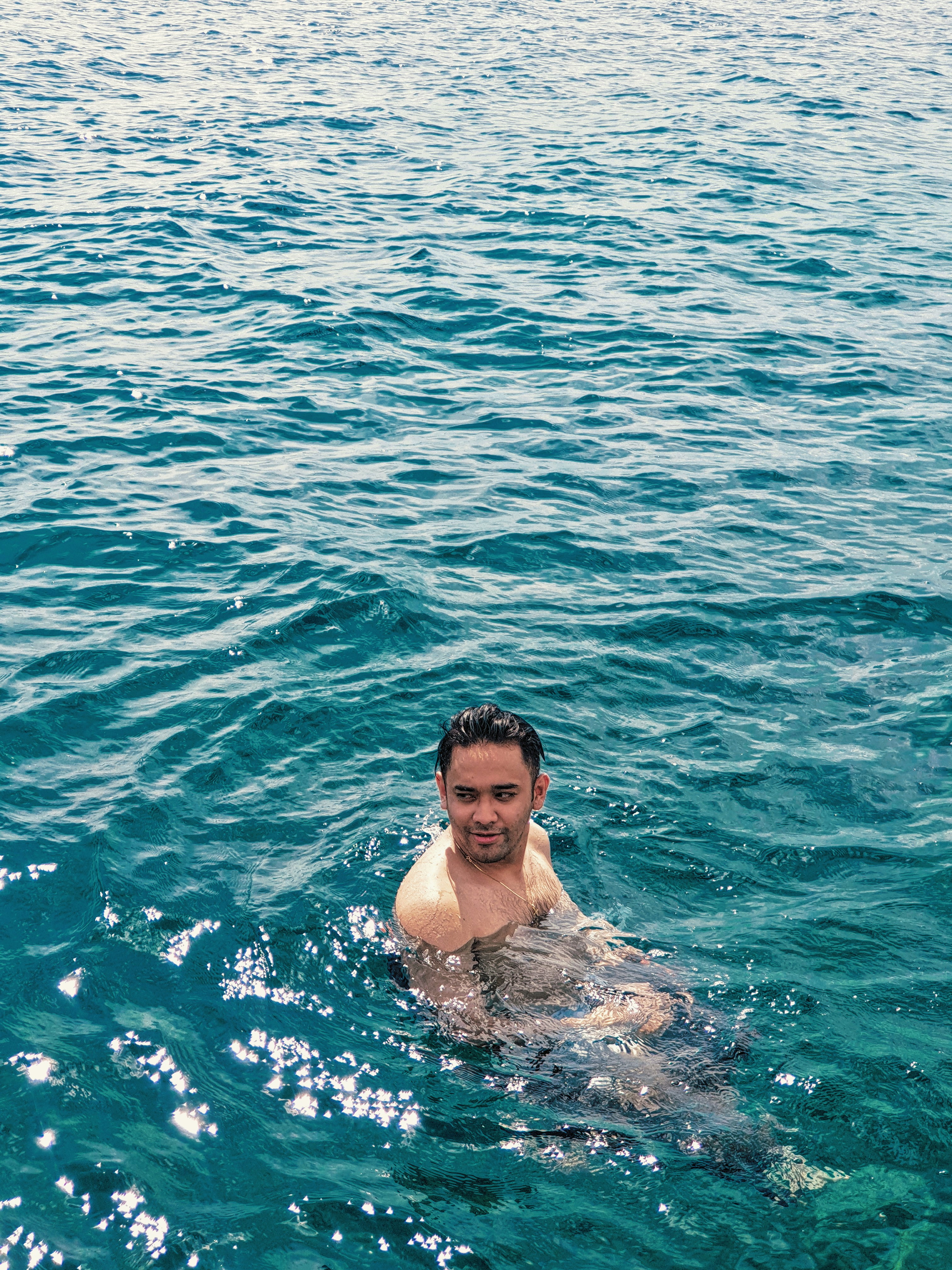 A man enjoys a refreshing swim in crystal-clear turquoise waters, surrounded by gentle ripples and sunlight reflections.
