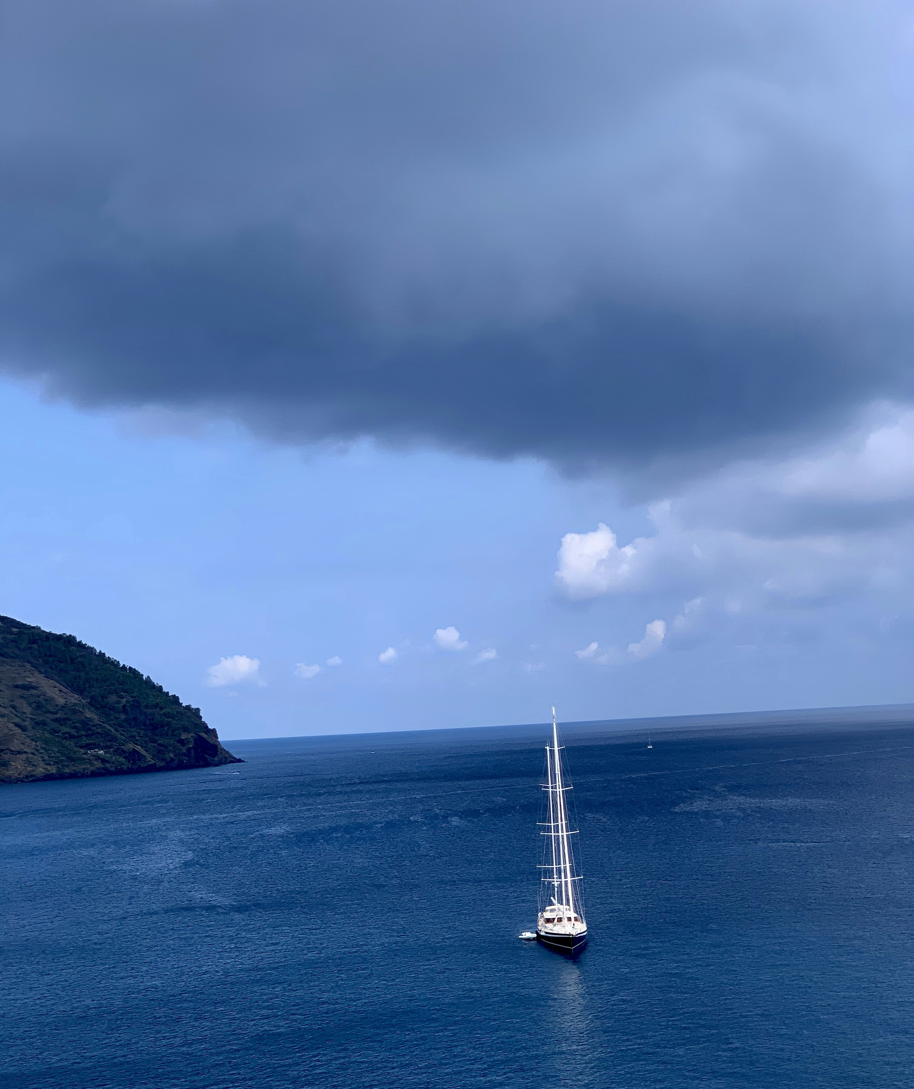 Solitary Sailboat Drifting Across a Velvet Blue Sea Beneath a Heavy Sky
