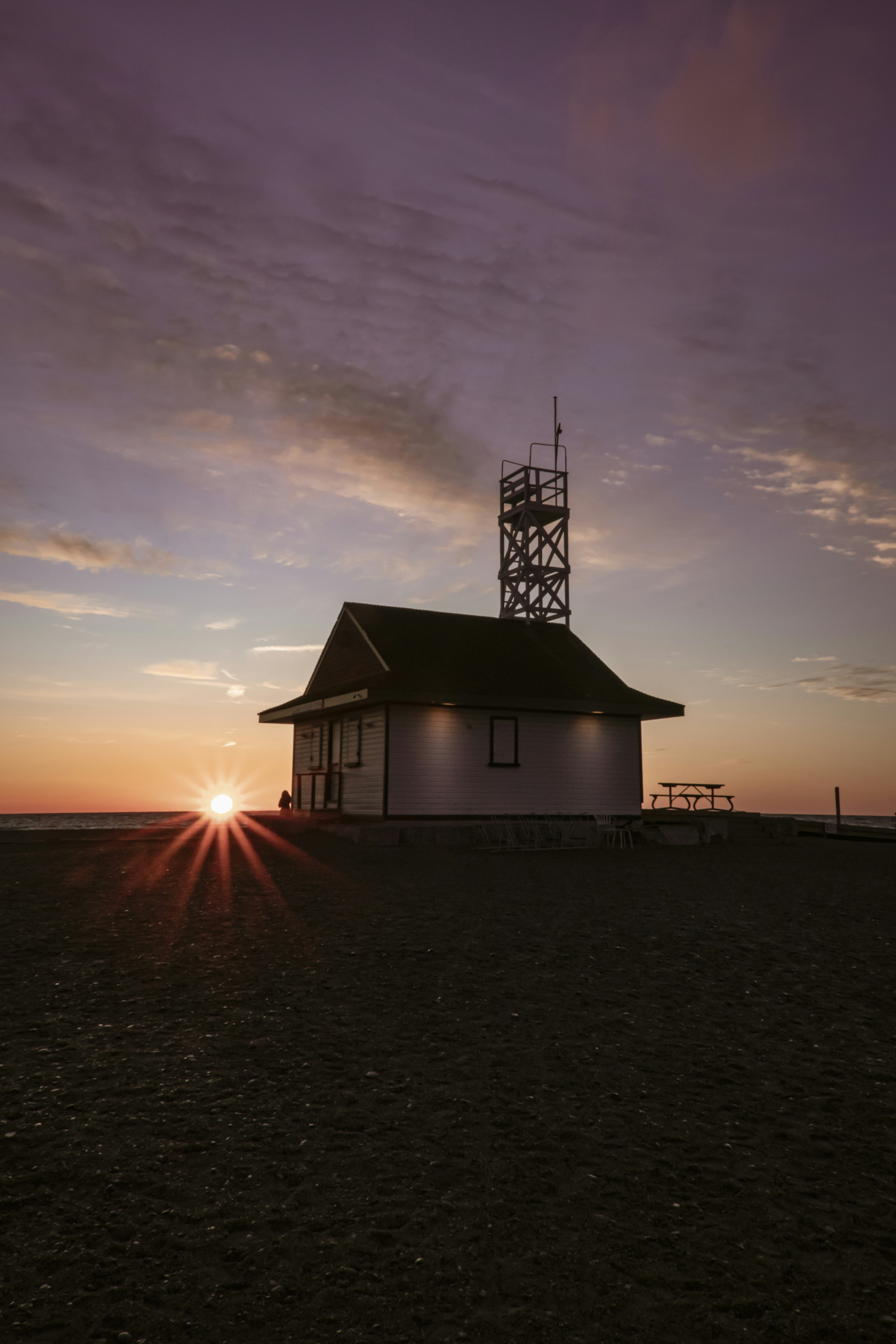 The sun breaks the horizon behind a lifeguard station