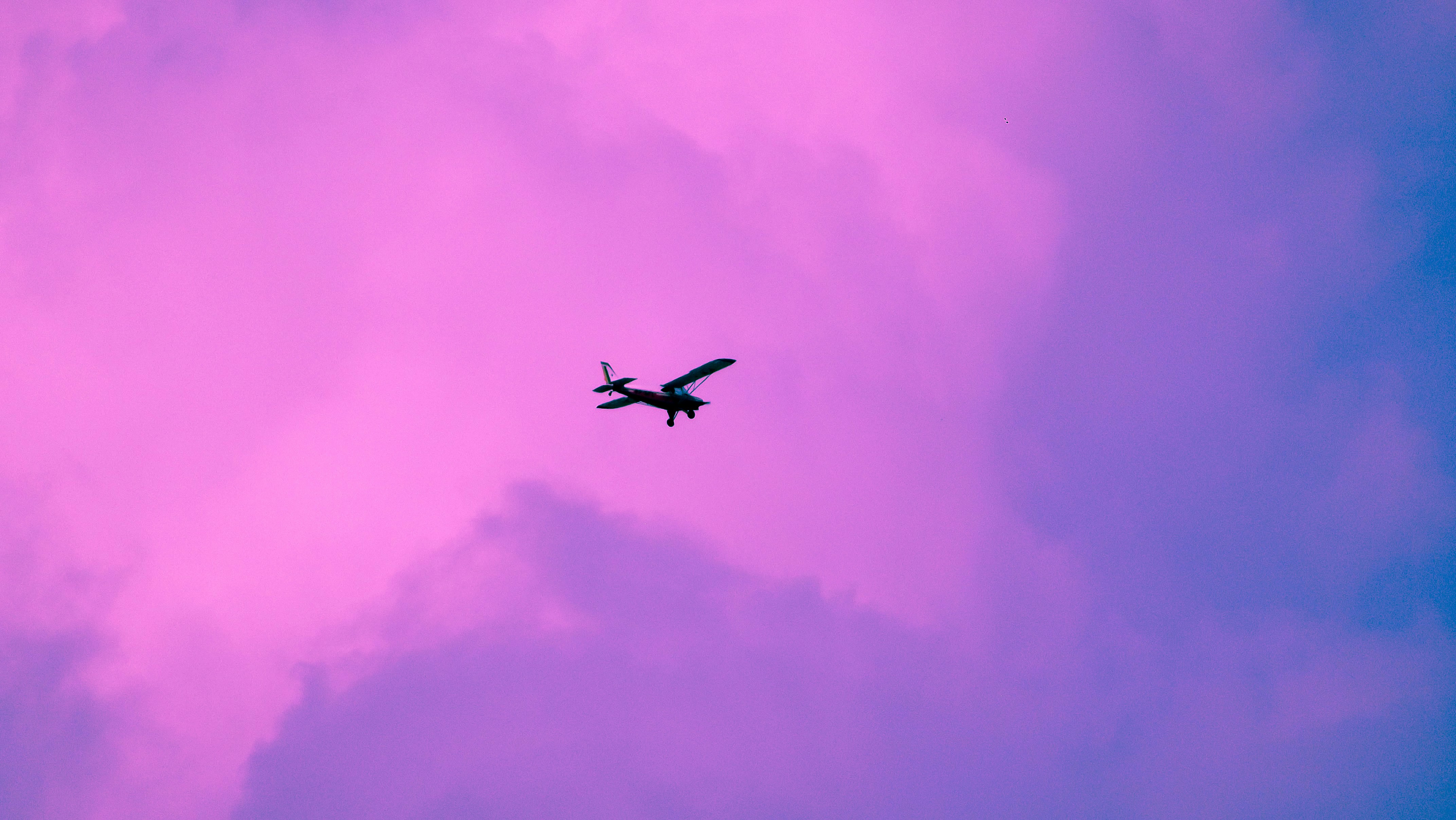 Silhouette of an airplane soaring through a vibrant, lavender-hued sky filled with soft clouds.