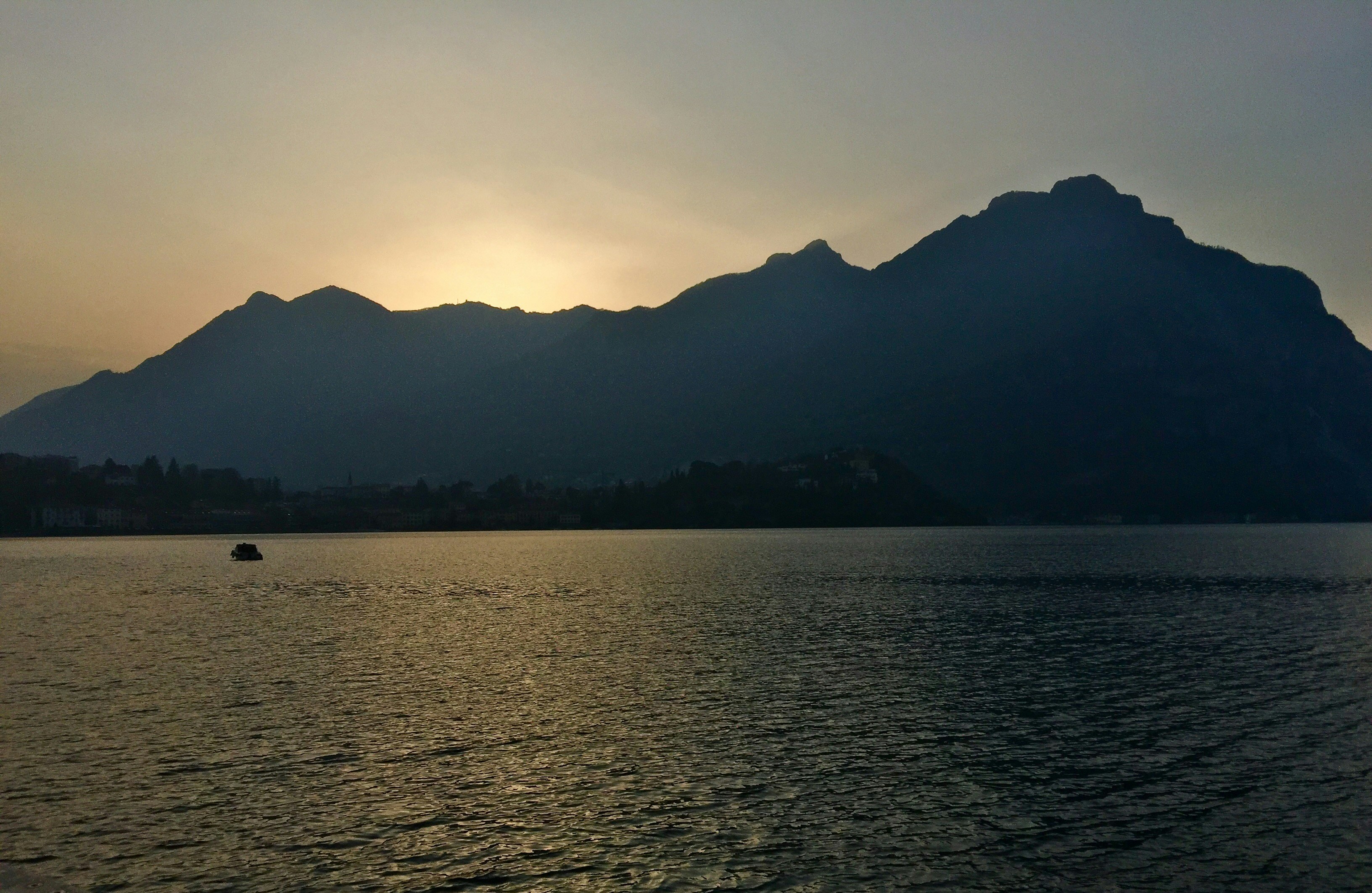 Silhouette of a mountain range against a setting sun over calm waters.