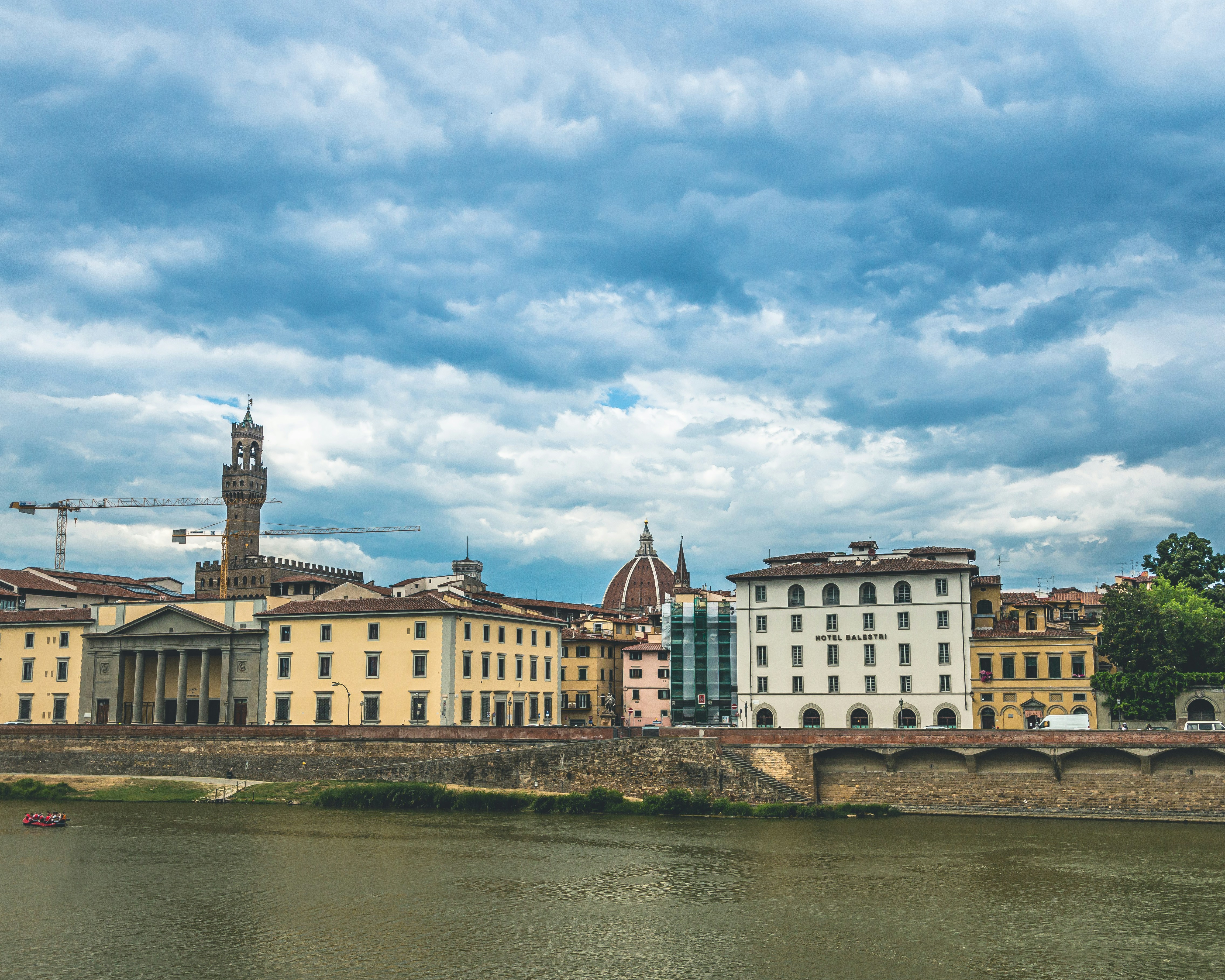 Historic buildings lining the Arno River in Florence, showcasing a blend of architectural styles against a dramatic sky.