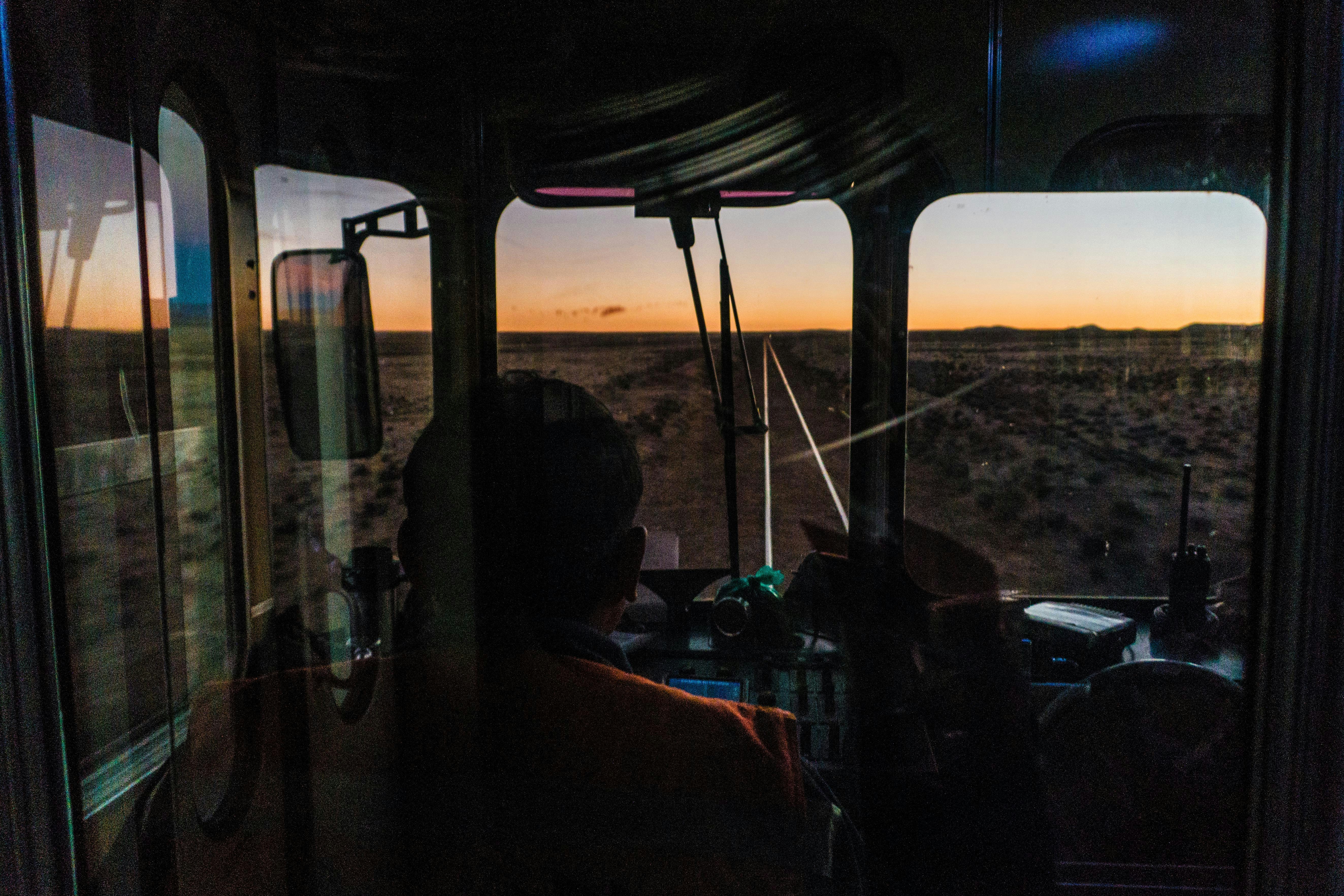 Silhouette of a person inside a vehicle at dusk, overlooking a vast desert landscape.