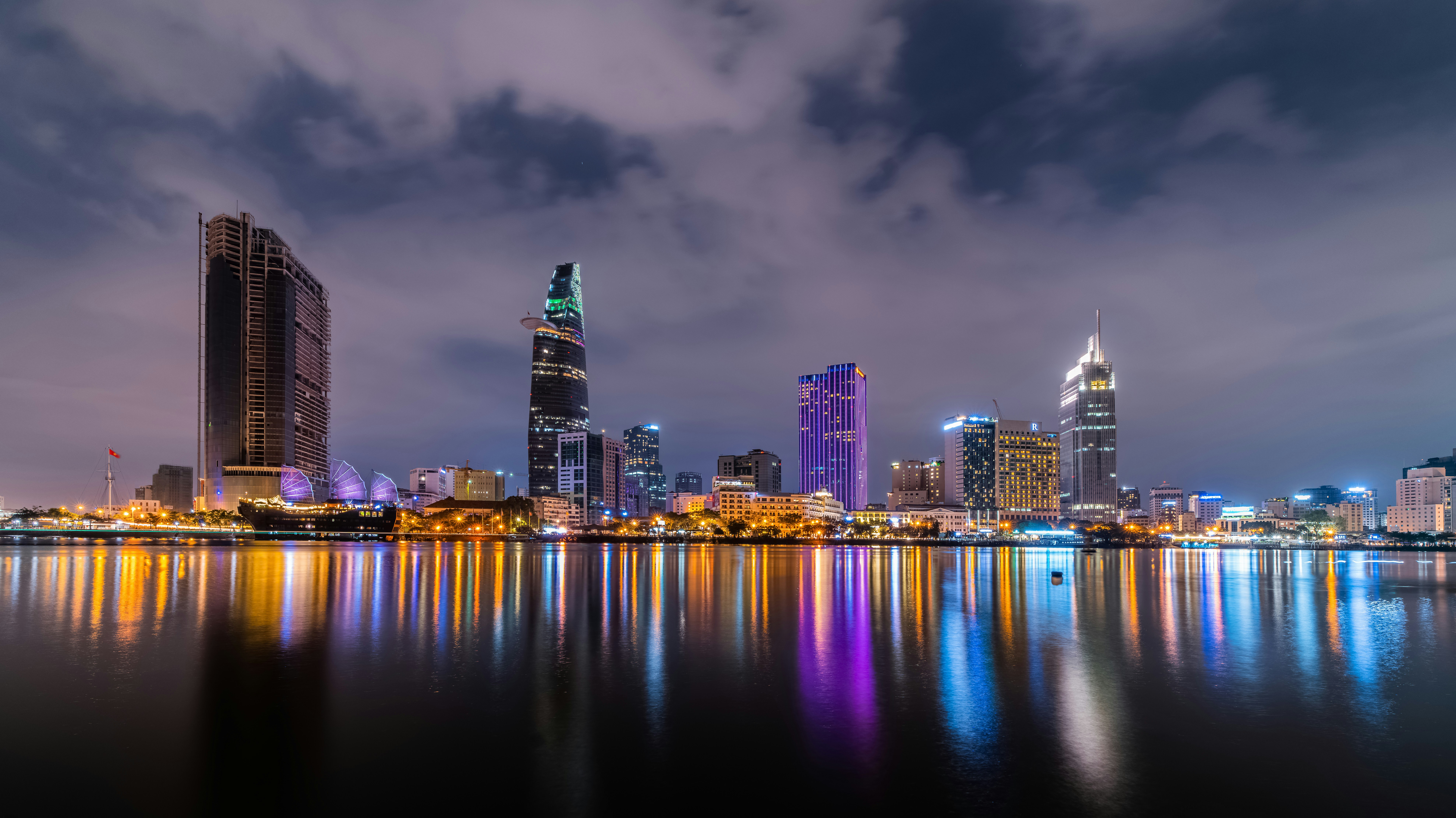 City skyline at night with colorful building lights reflecting on a calm river.