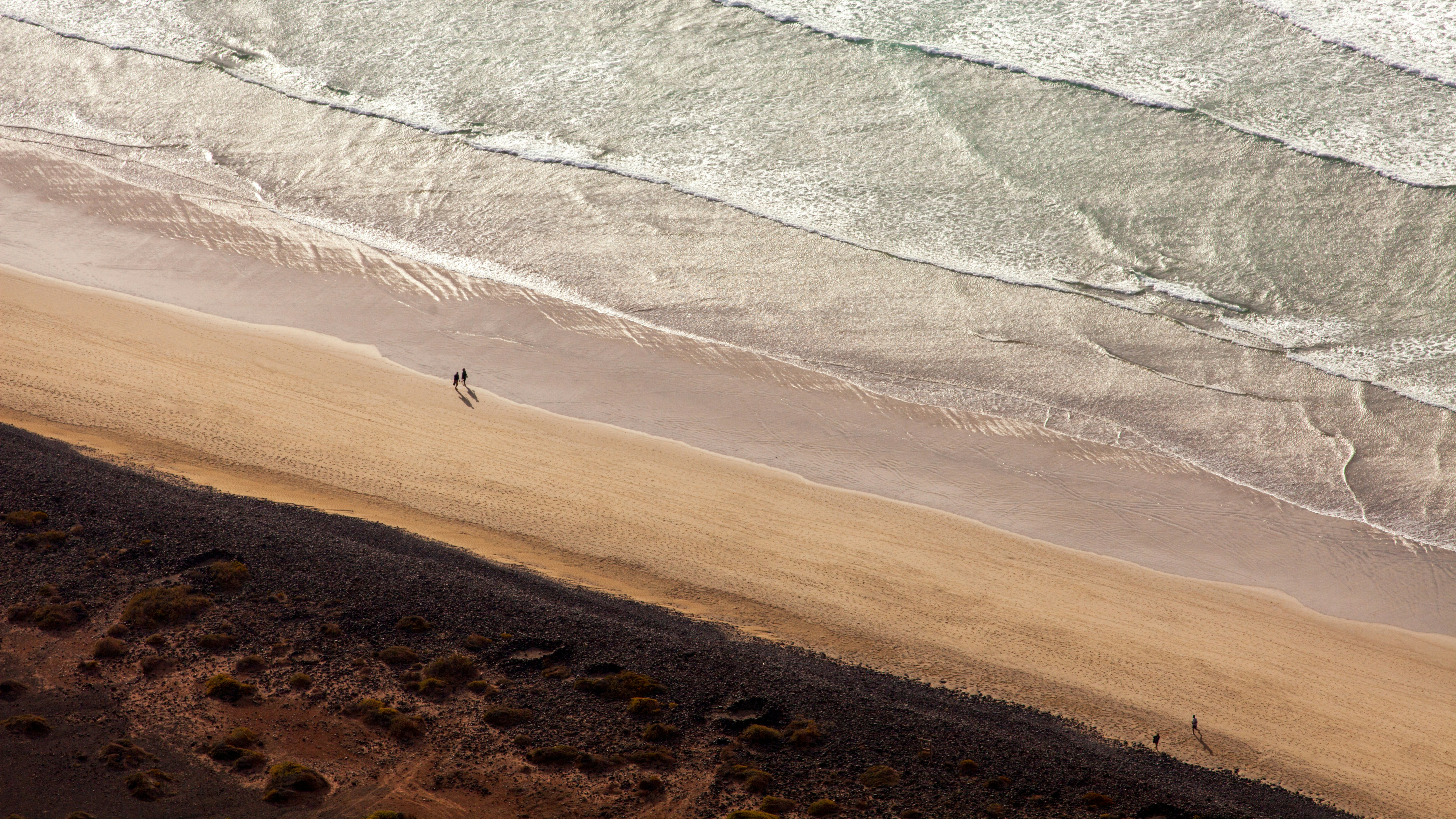 Aerial view of a lone figure walking on a sandy beach with waves rolling ashore.