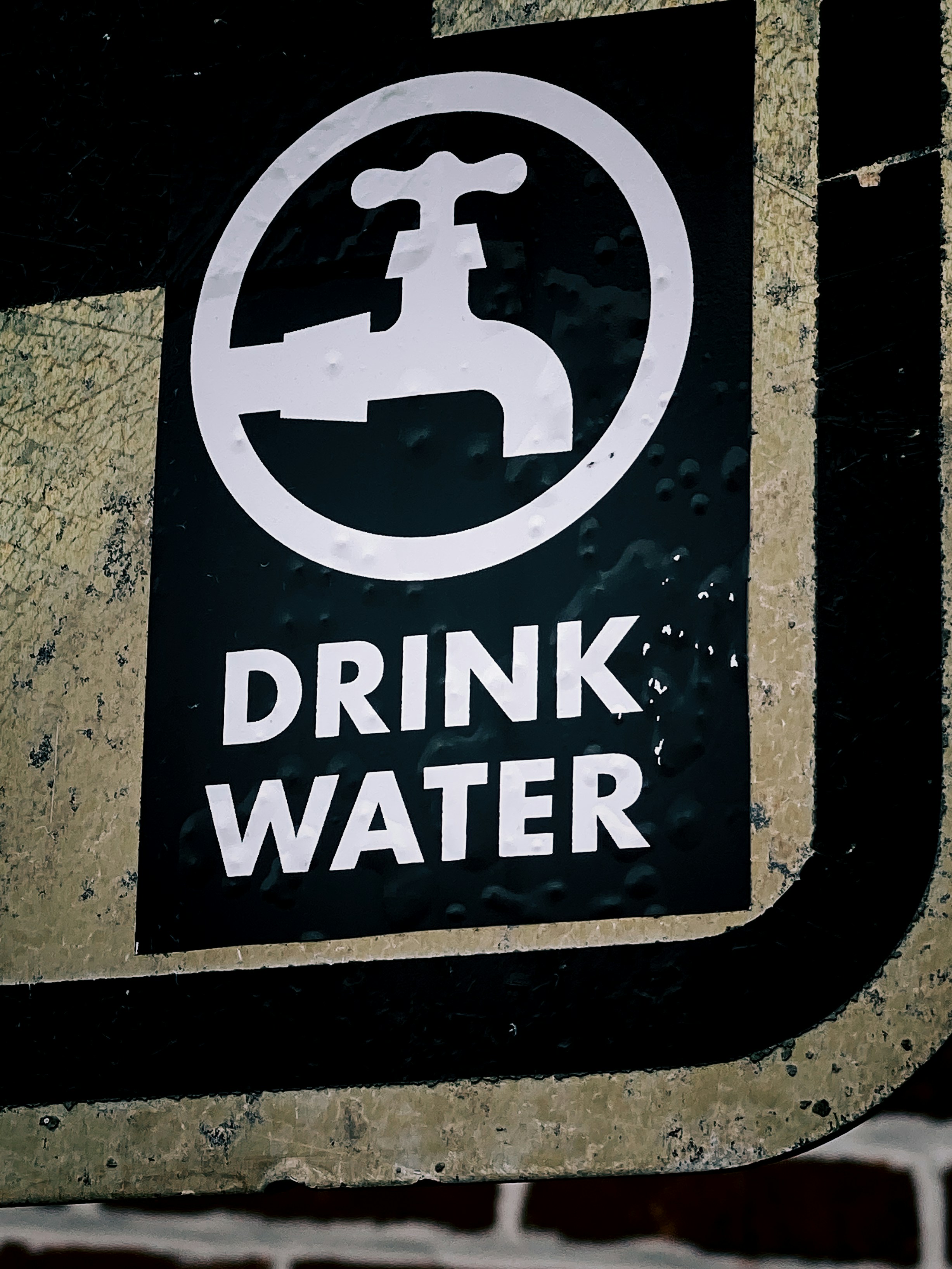 A black and white sign featuring a faucet icon and the text 'DRINK WATER', emphasizing the importance of hydration.