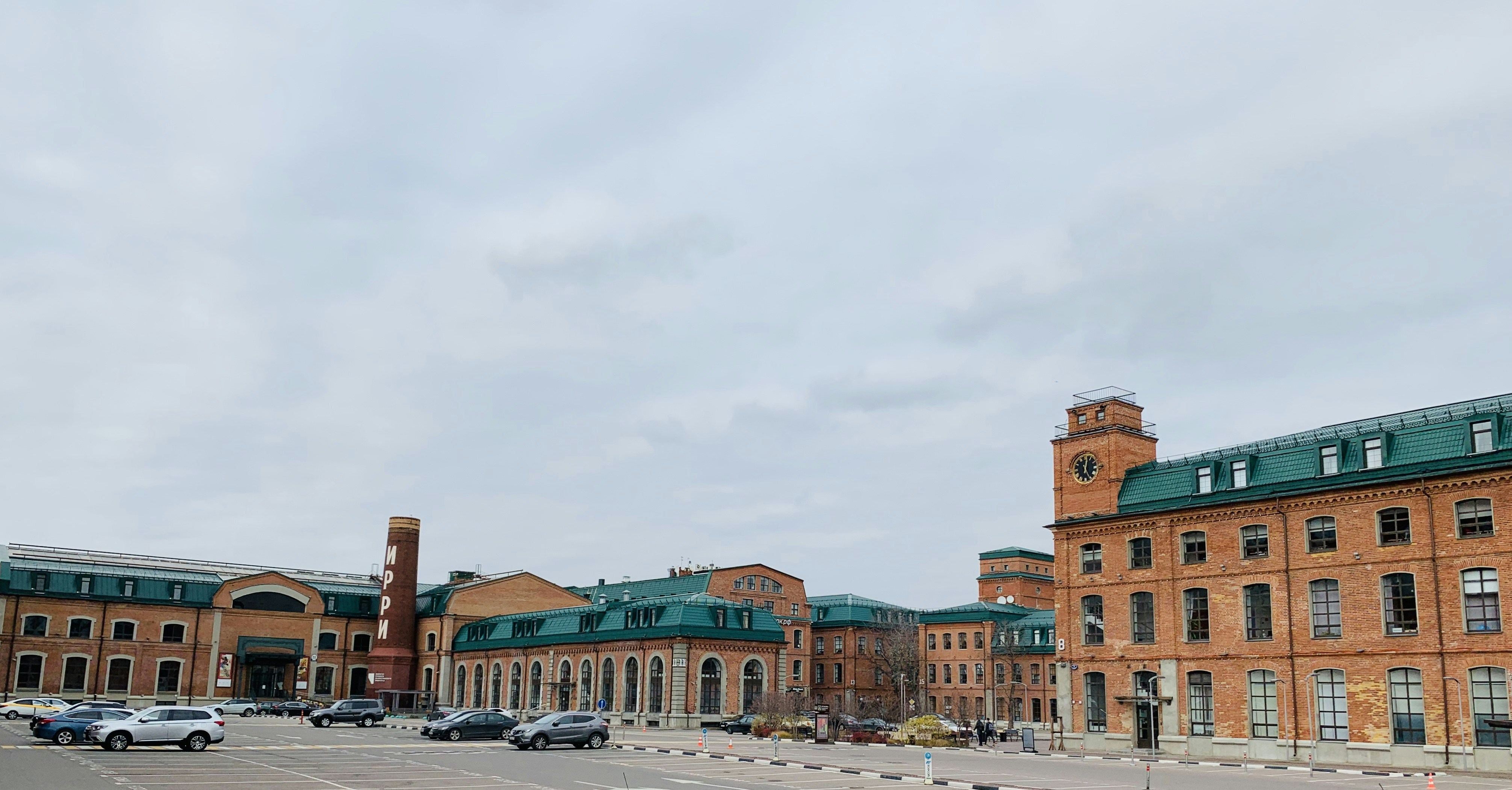 Historic brick buildings with green roofs and clock tower in an urban setting, showcasing architectural grandeur and a hint of nostalgia.