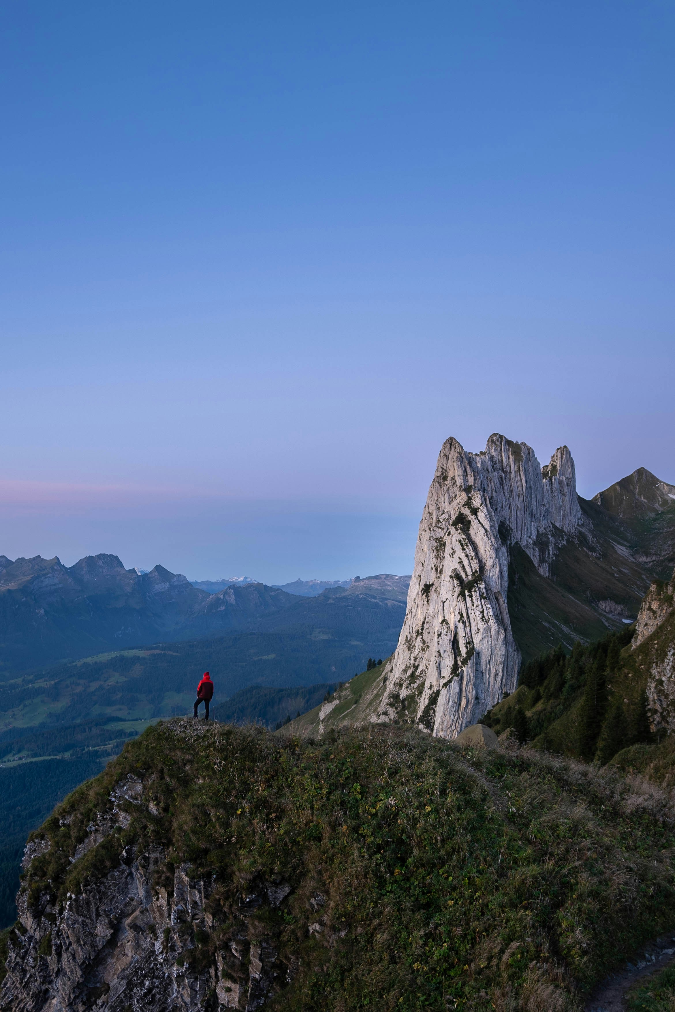 Men standing on cliff next to blue hour mountains | person standing on cliff