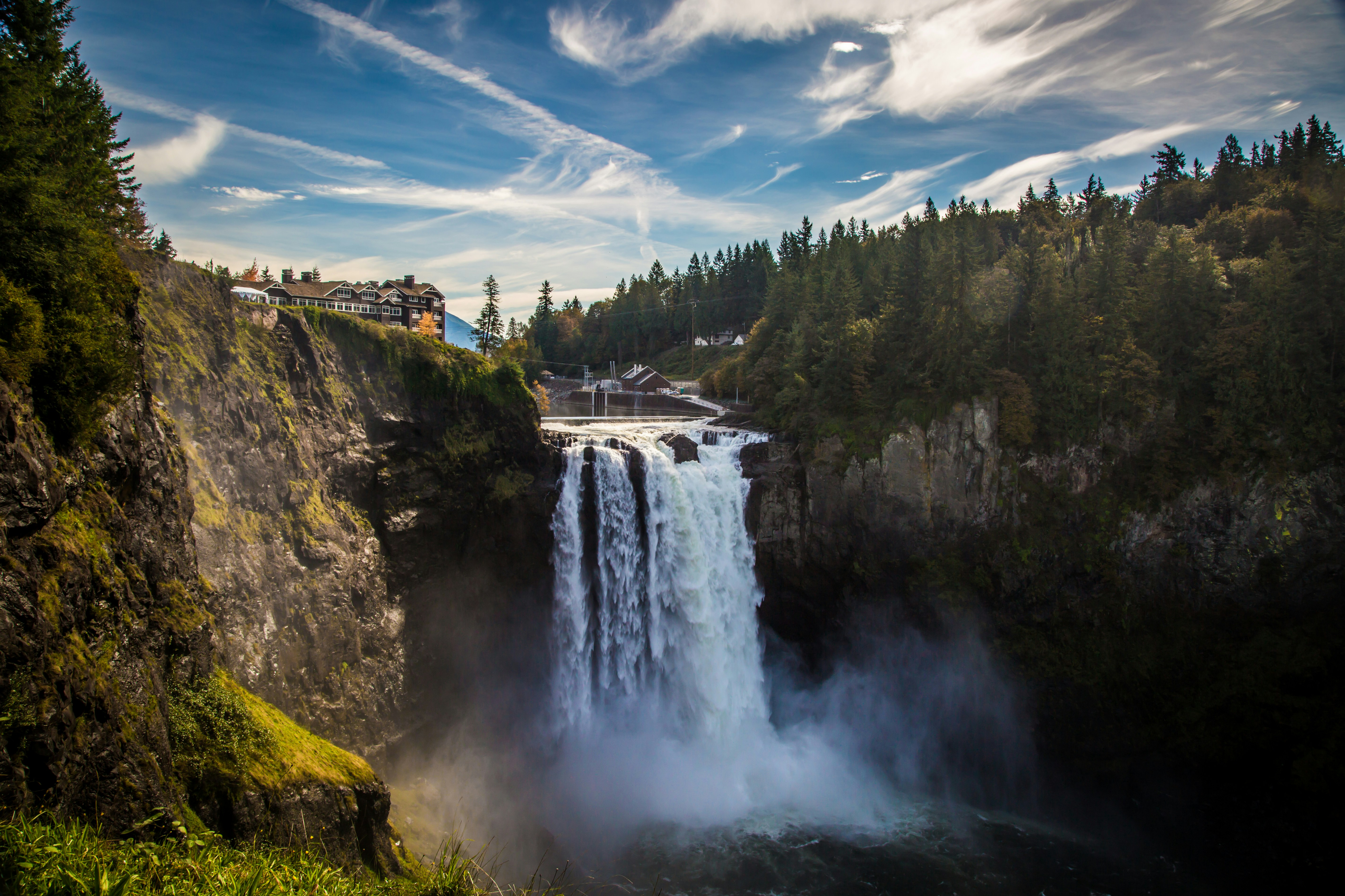 Majestic waterfall plunging into a misty gorge, surrounded by lush greenery and a distant observation area. A blend of natural beauty and human presence.